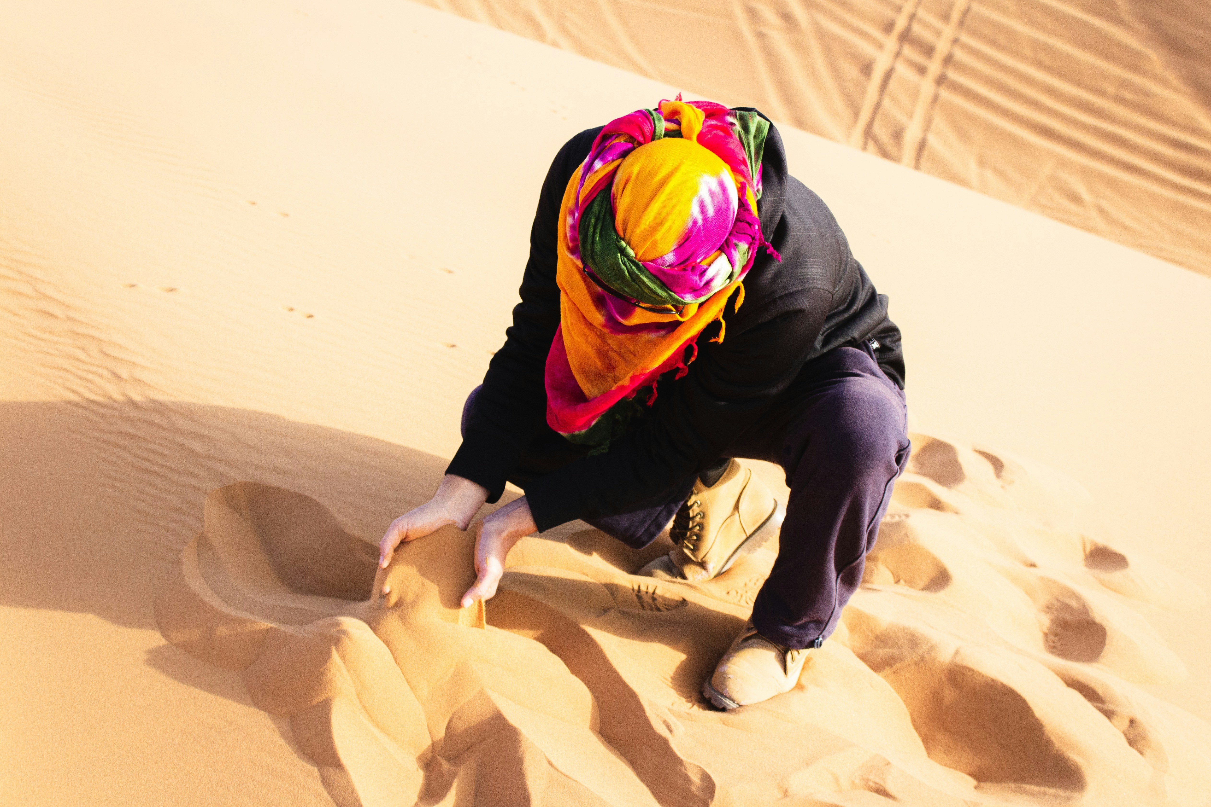 Desert Portrait: A Figure in Colorful Turban Crouches Amid Golden Dunes