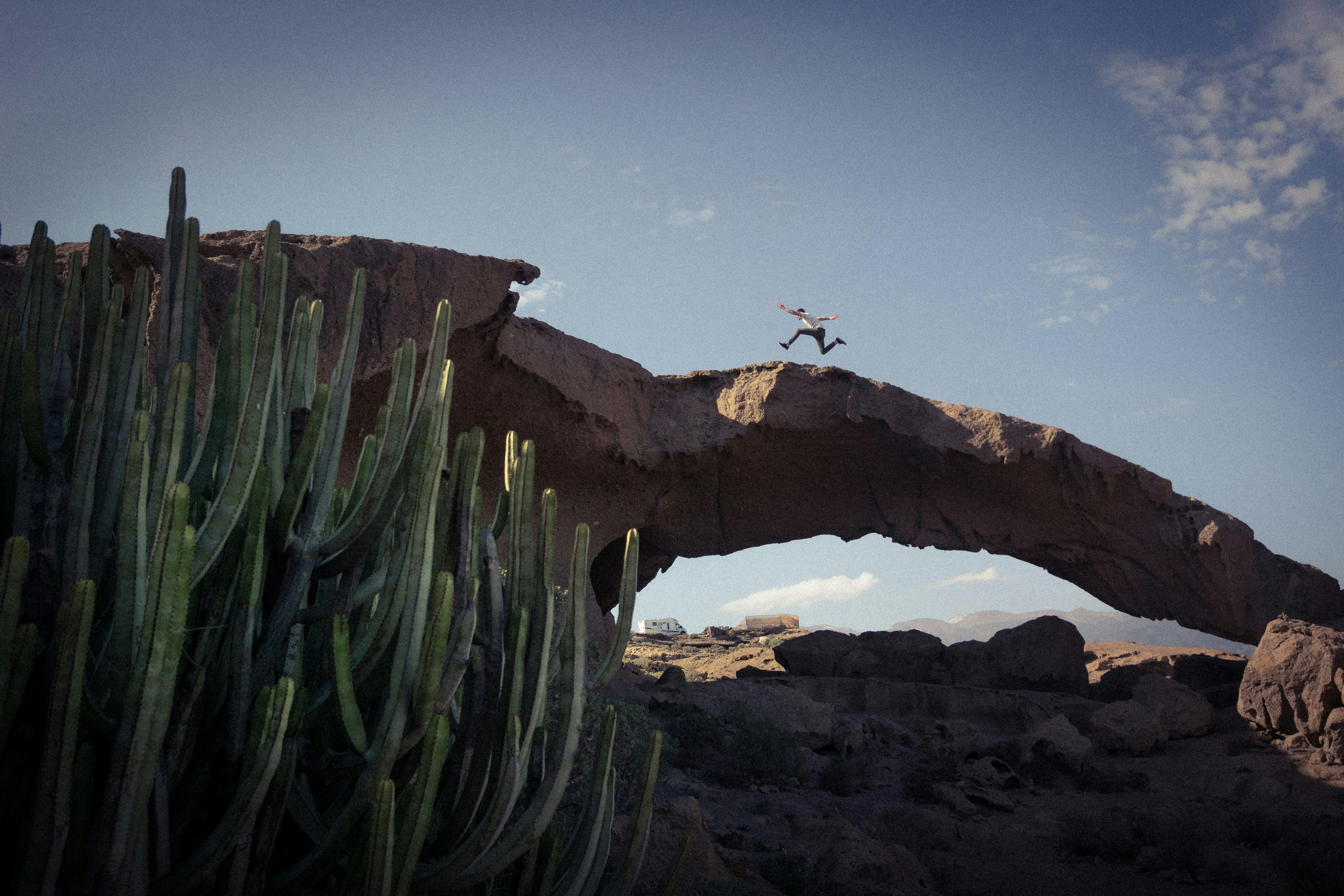 Man leaping on rock arch formation under blue sky photo – Free Grey ...