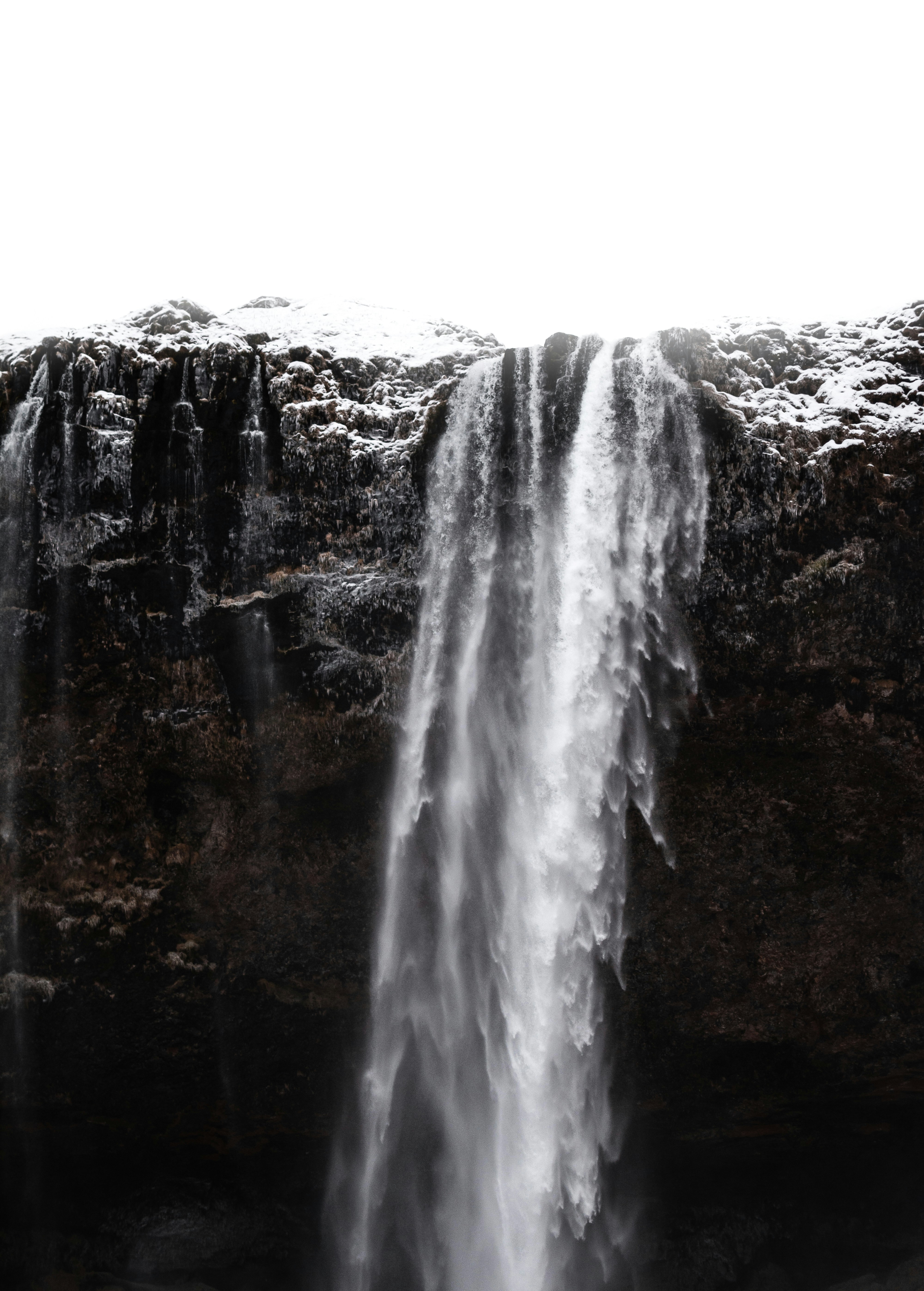 Waterfall cascading down rugged cliffs, surrounded by a snowy landscape, creating a mesmerizing contrast between water and ice.