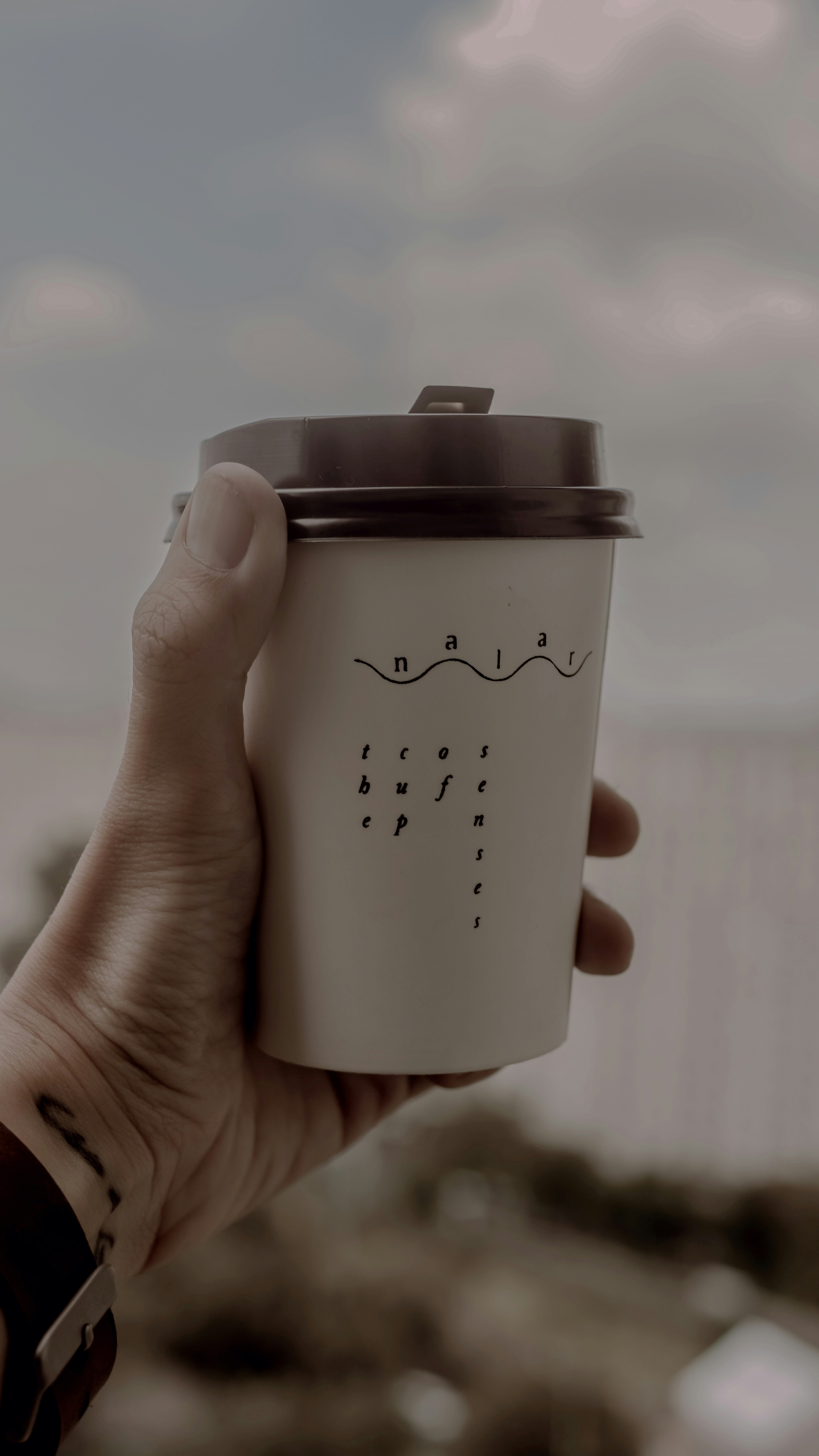 A Warm Cup in Focus: Handheld Coffee Moment Against a Soft Sky