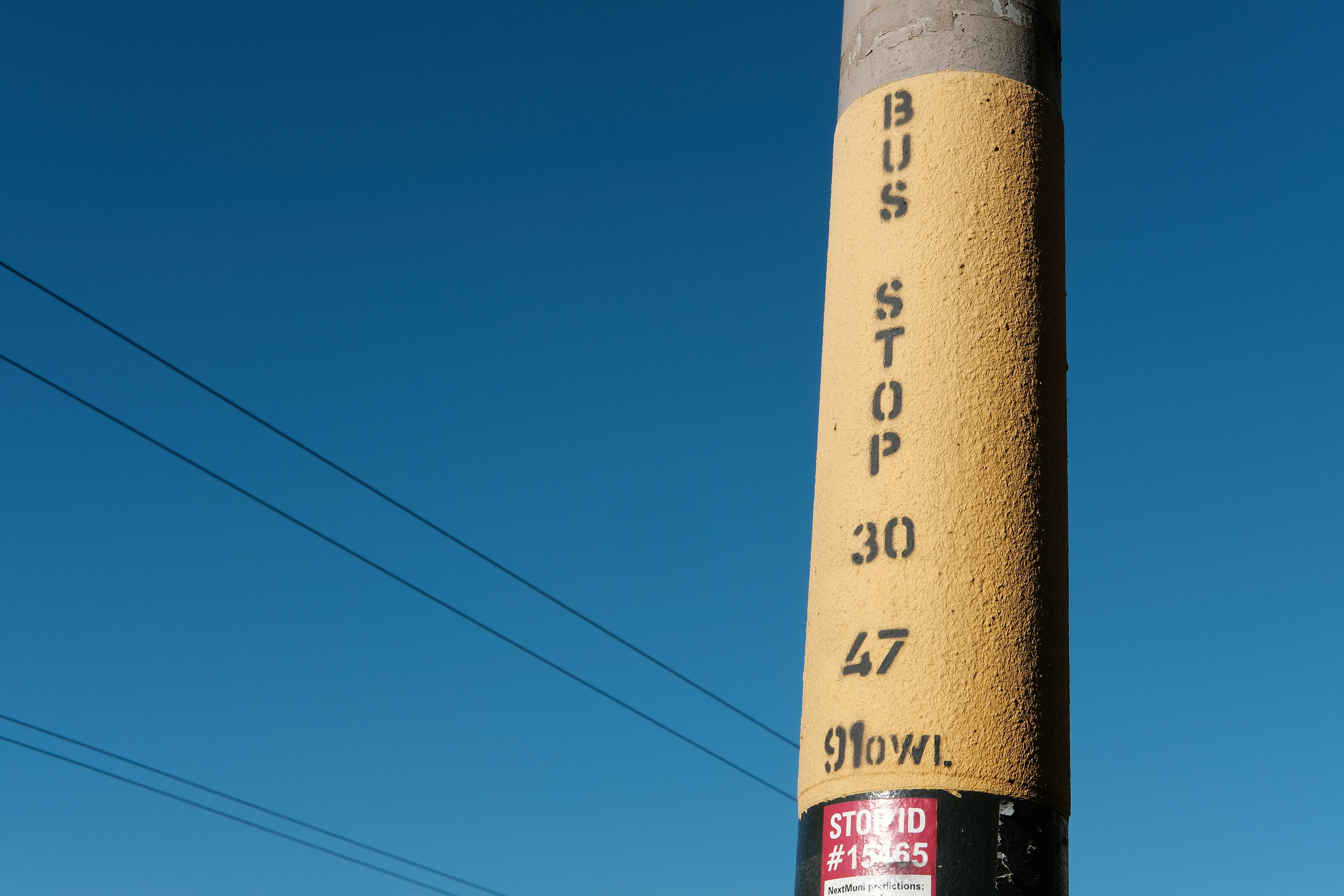 Yellow Bus Stop Pole Reaching Toward a Clear Blue Sky