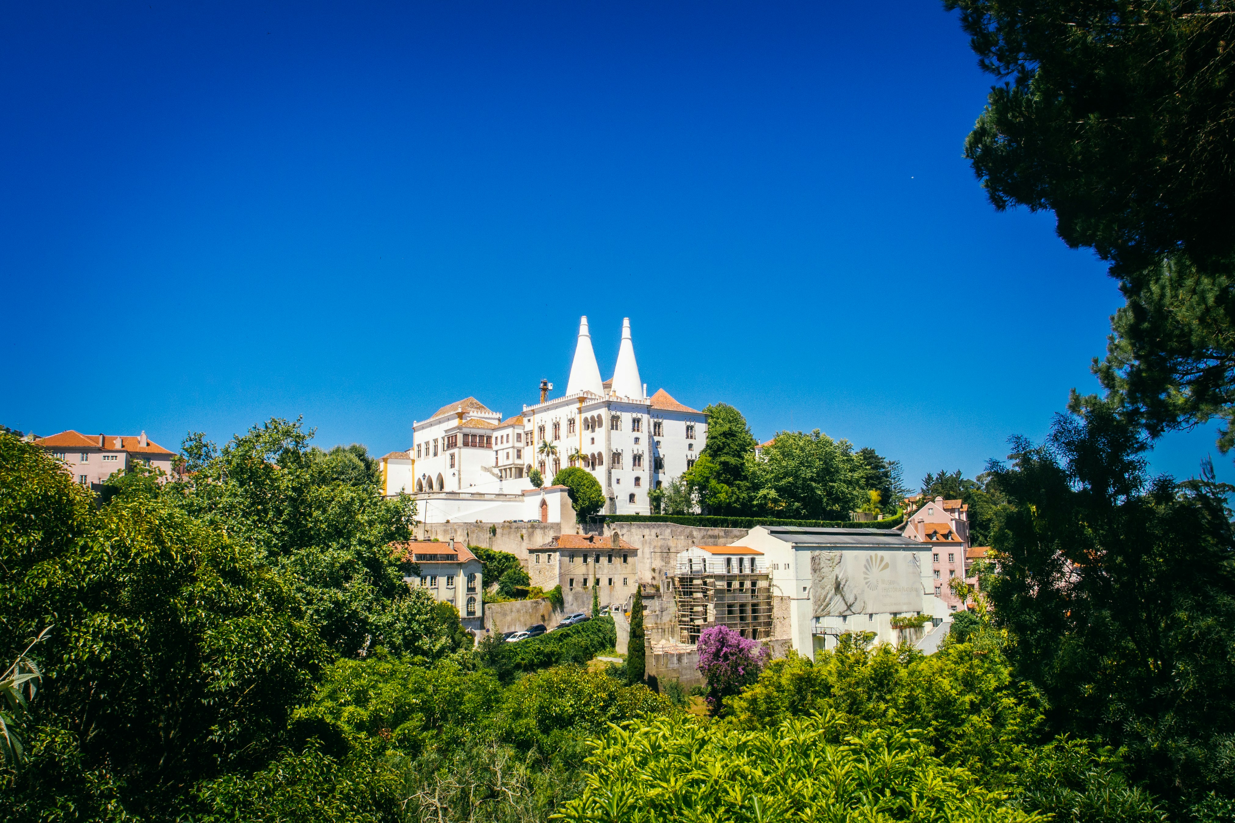 Historic building atop a lush hillside, surrounded by vibrant greenery and a clear blue sky.