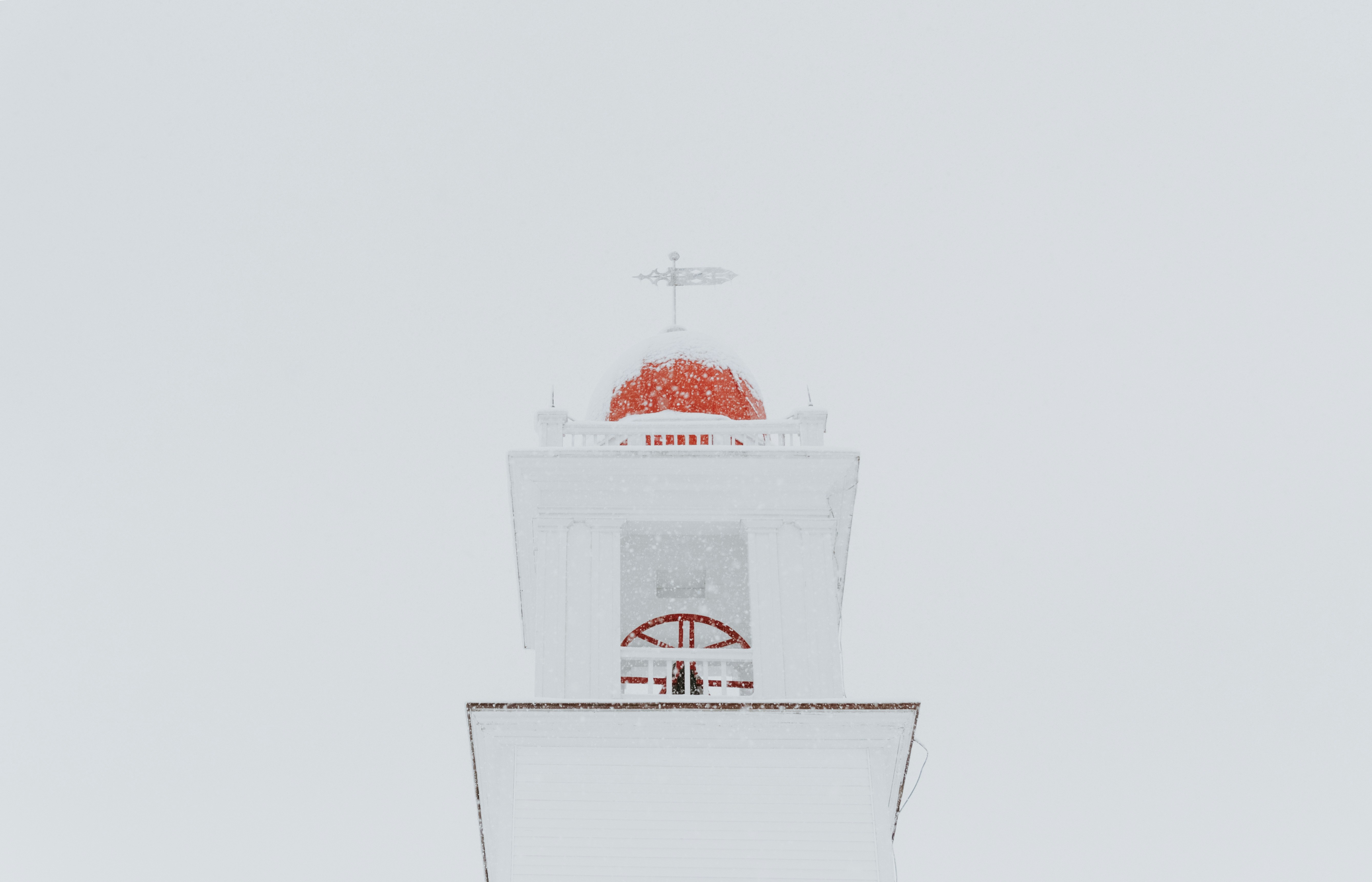 A weathered clock tower adorned with a vibrant red dome, emerging from a blanket of snow in a tranquil winter landscape.