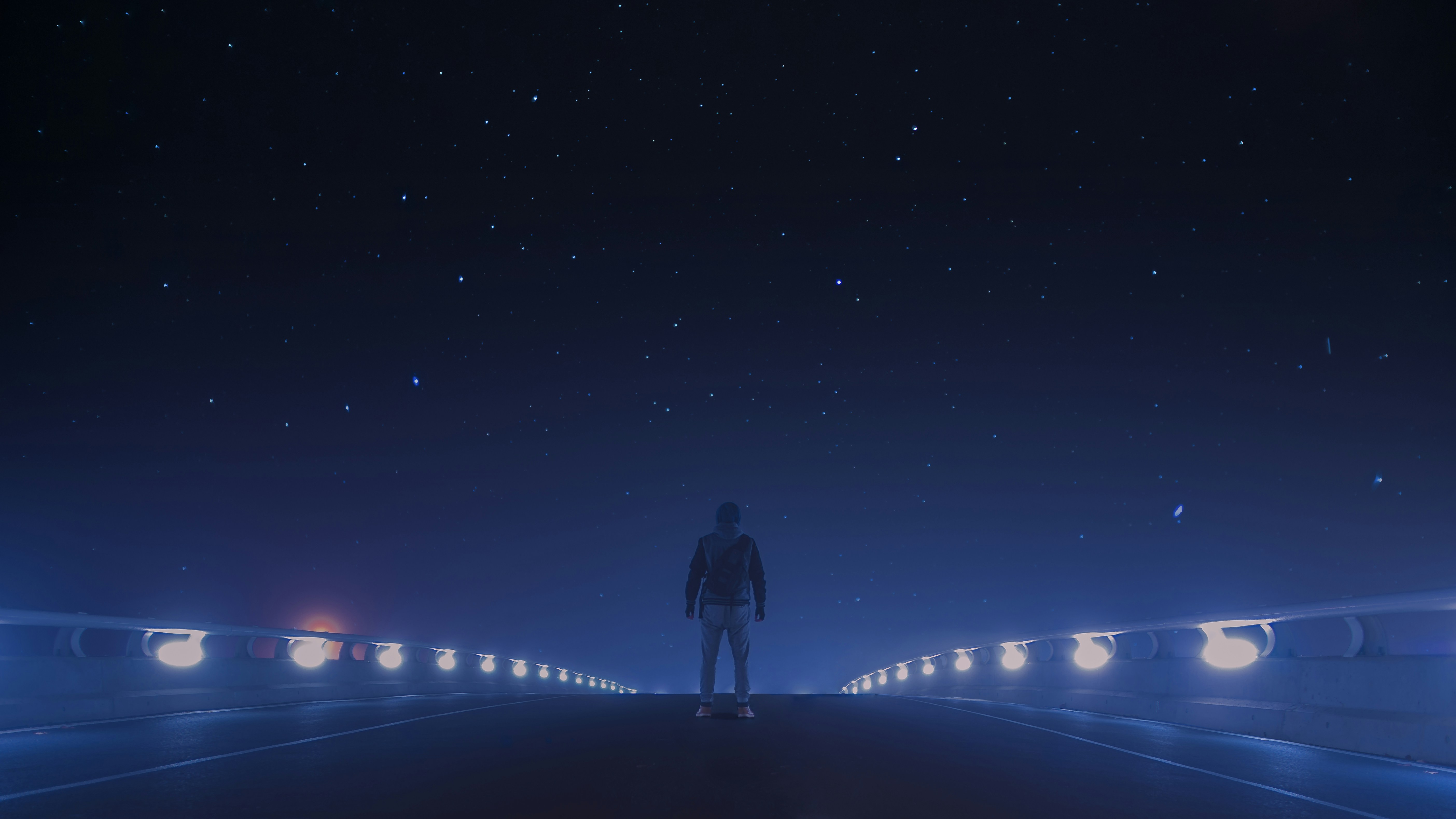 Silhouette of a person standing on a bridge illuminated by blue lights beneath a starry night sky.