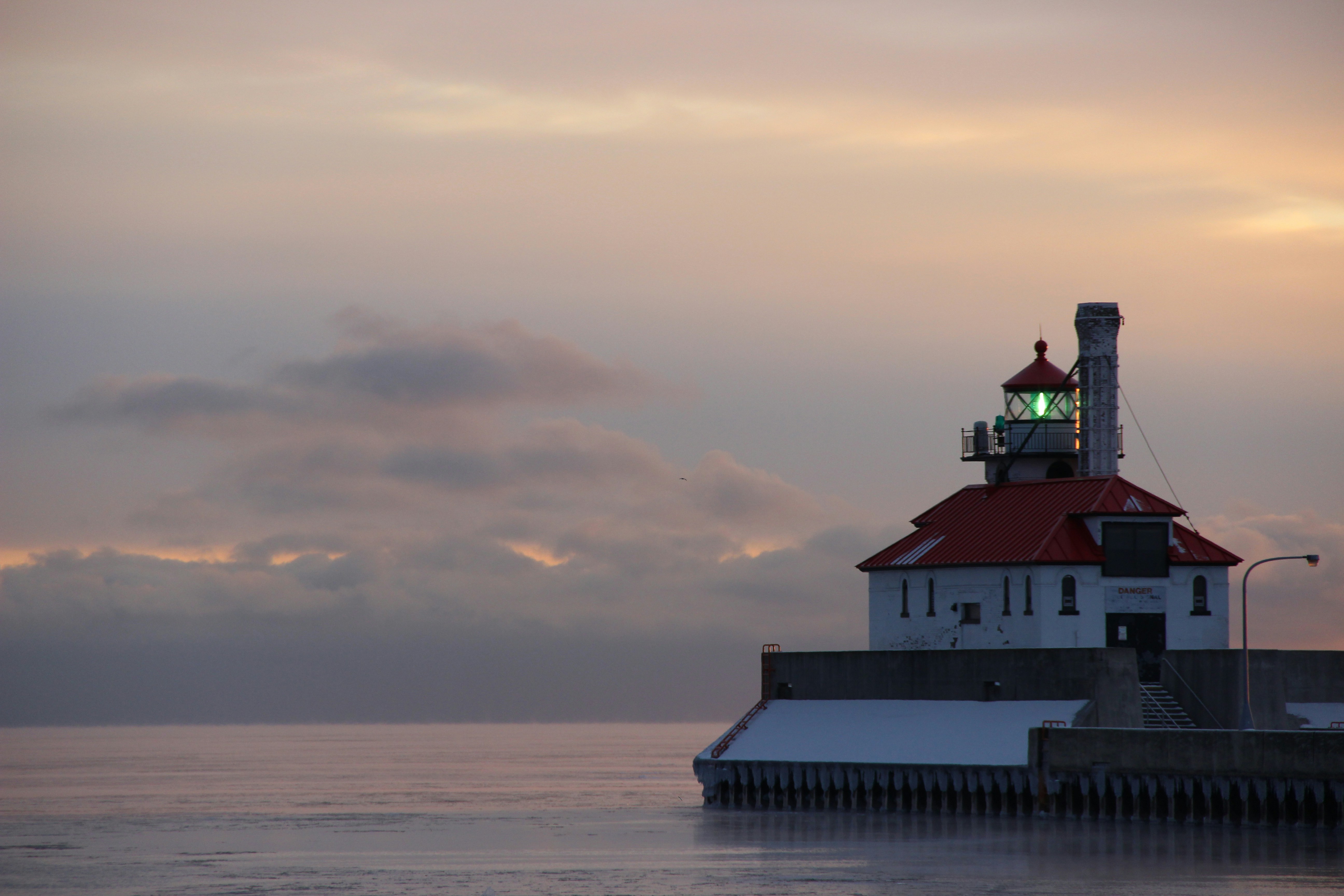 Lighthouse with a red roof stands against a serene evening sky over calm waters.