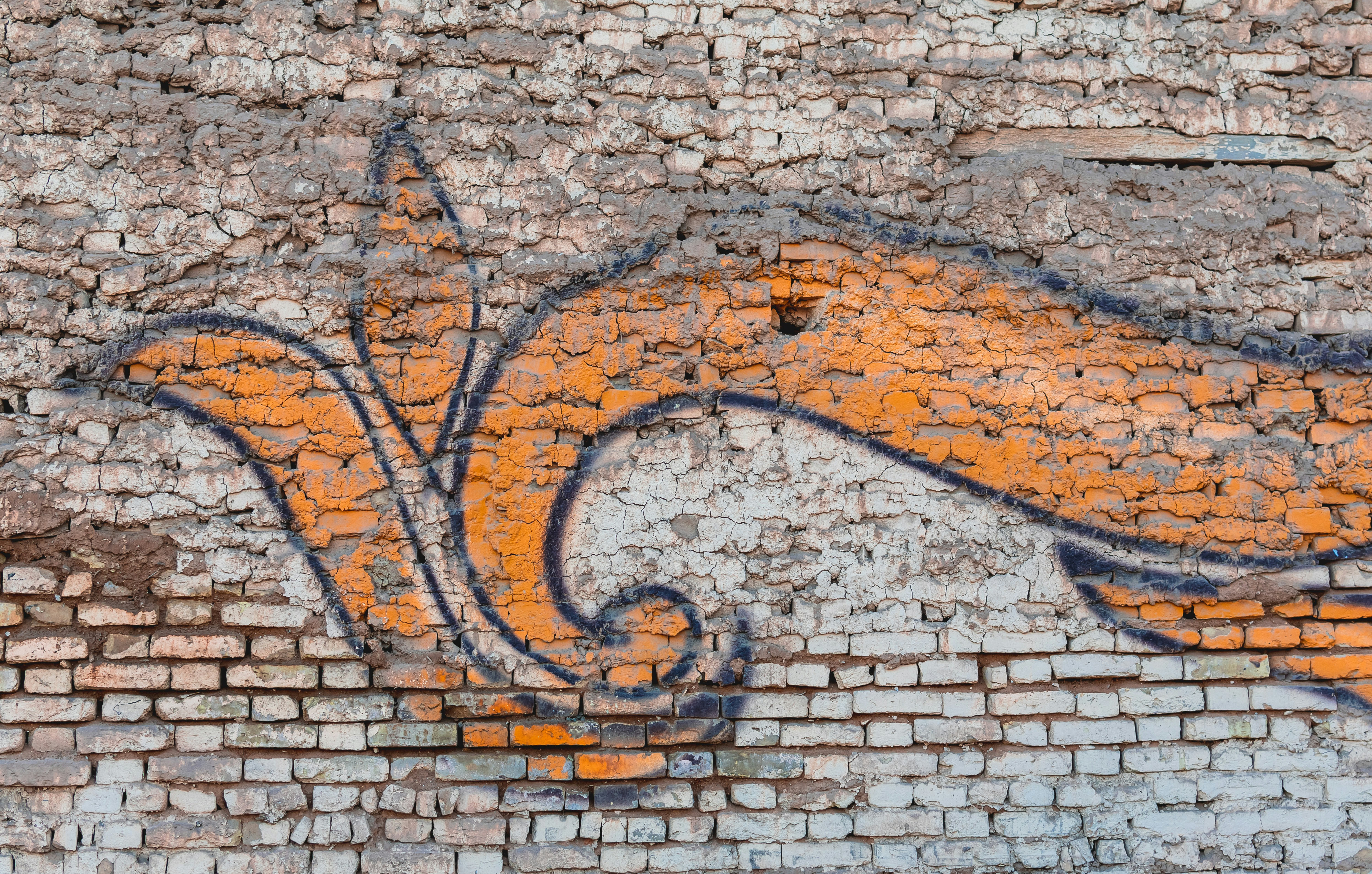 Vibrant orange graffiti swirls across a weathered brick wall, showcasing urban art's interplay with decay. The intricate design contrasts starkly with the rough surface.