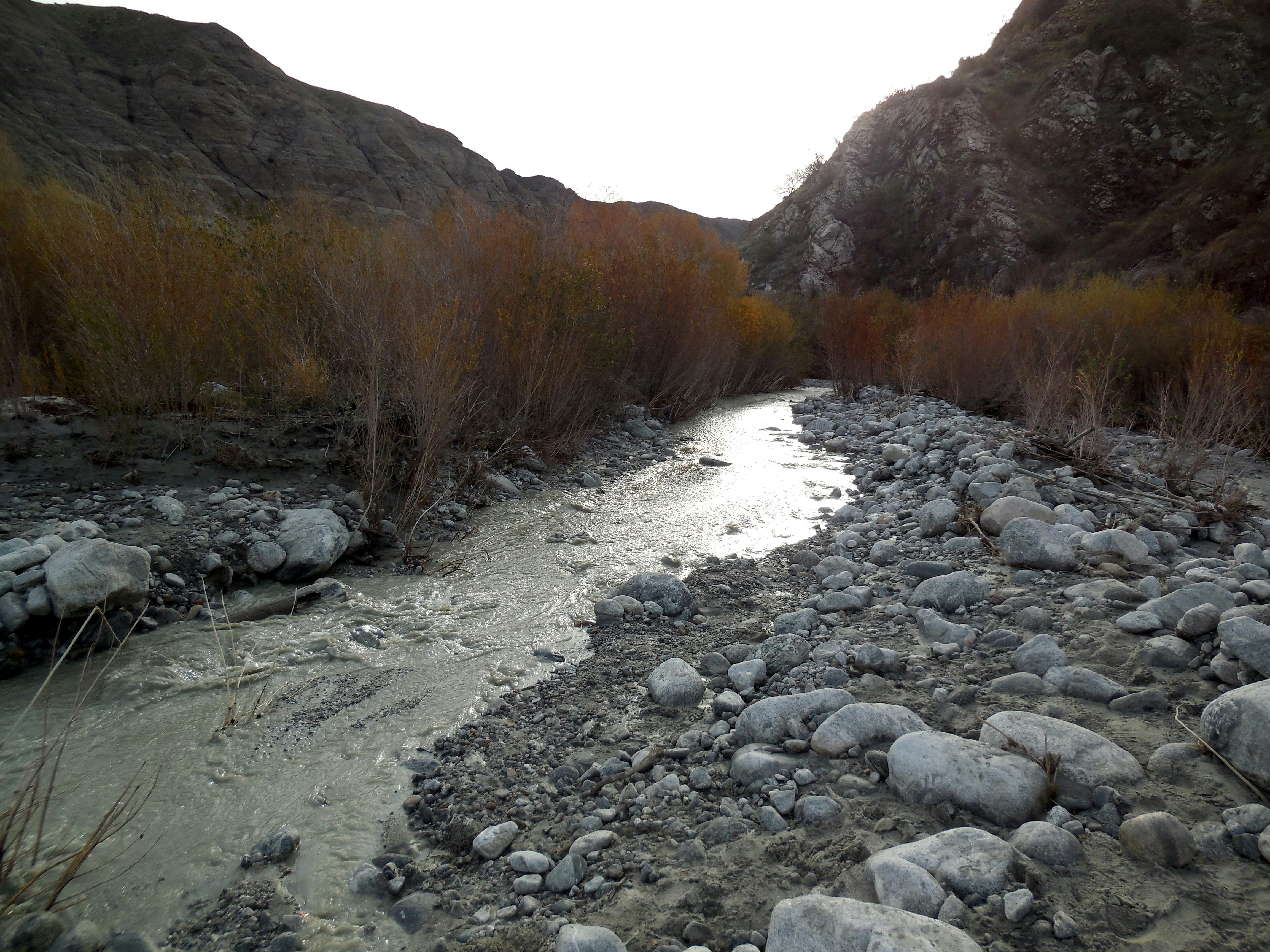 Rocky stream winding through a narrow canyon surrounded by sparse vegetation and rugged hills.