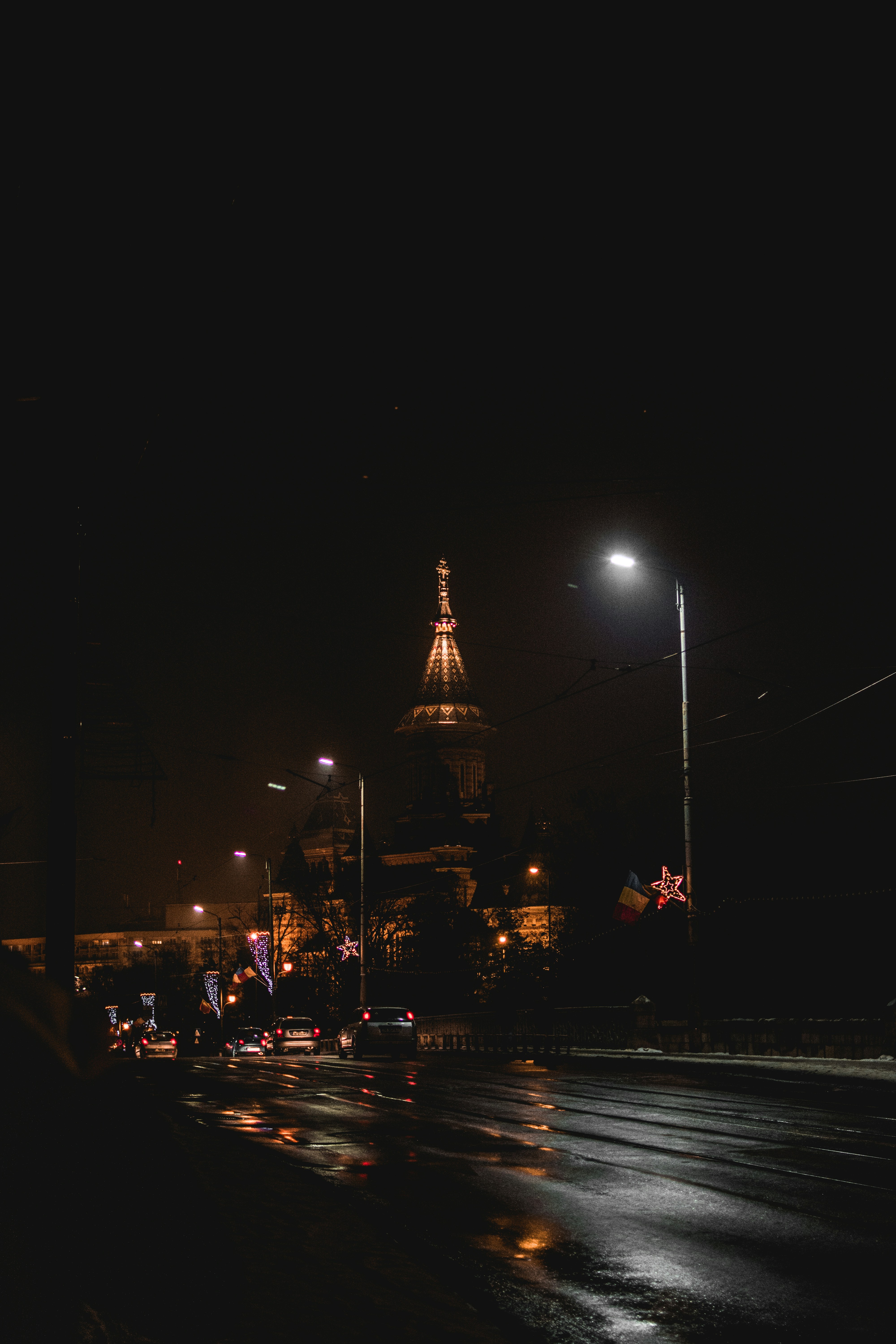 Historic building with a brightly lit spire emerges through the fog, reflecting on wet streets at night.