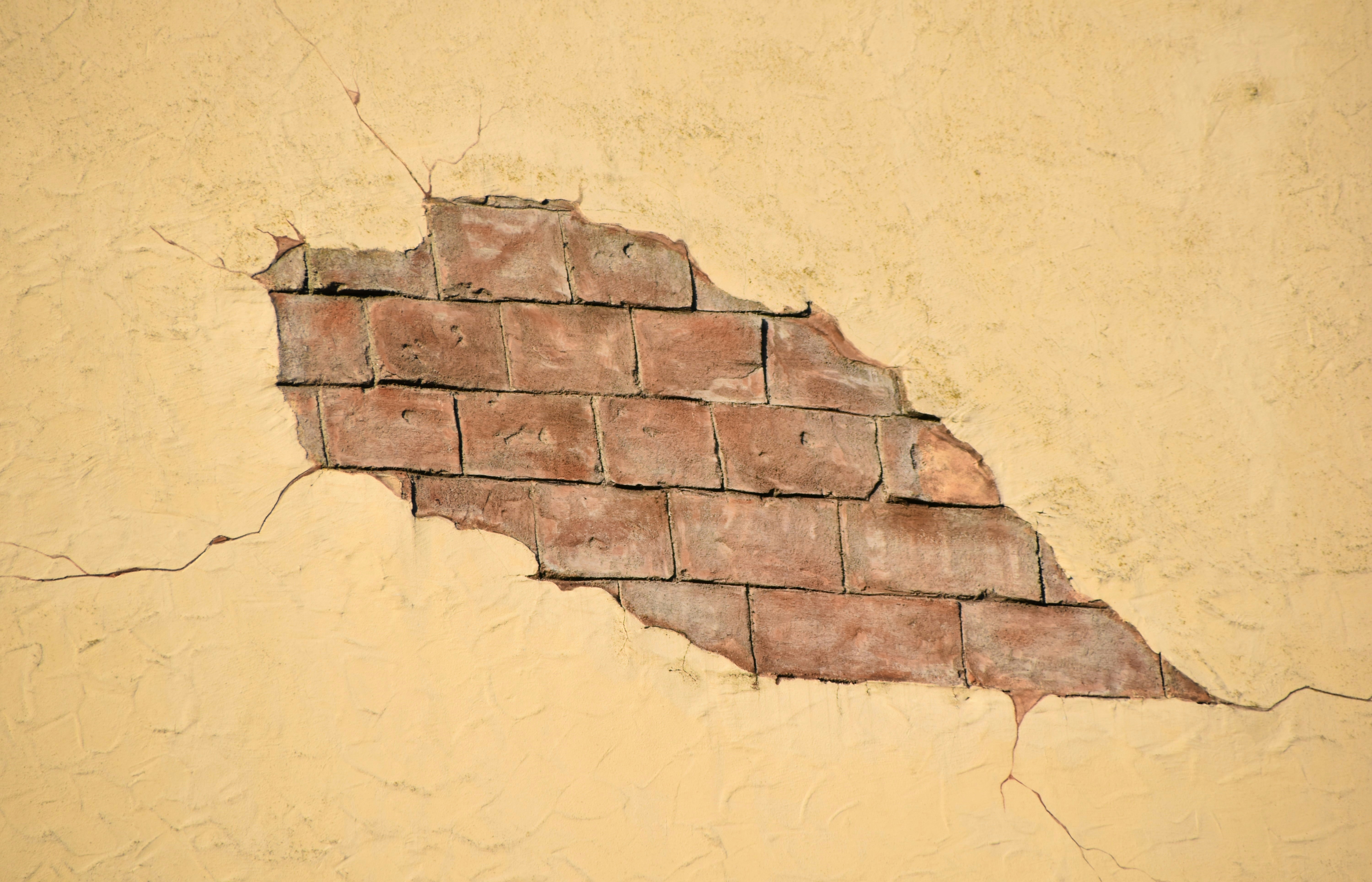 Exposed bricks reveal the underlying structure of a weathered wall, showcasing the contrast between the rough texture and the smooth surface surrounding it.