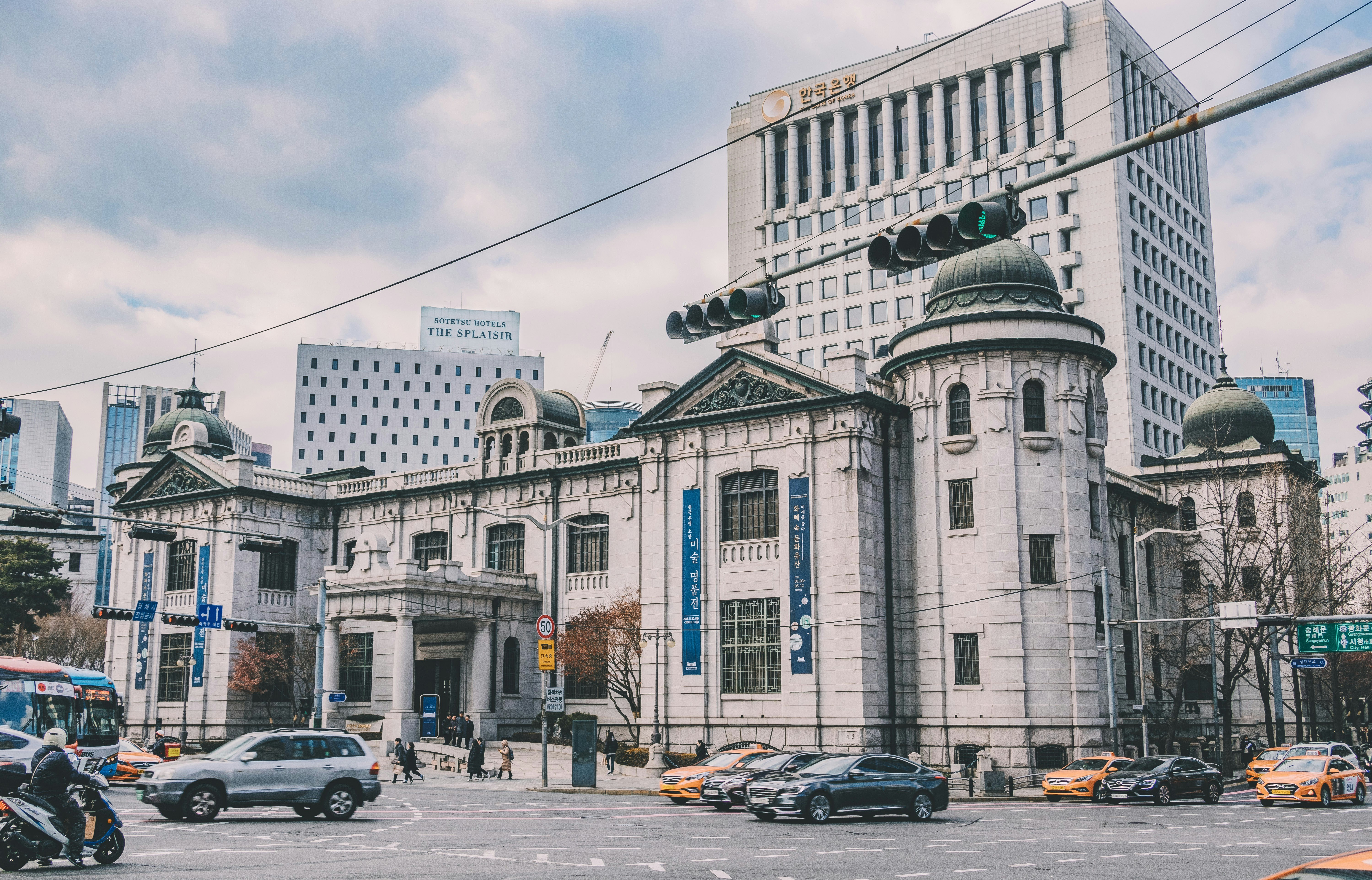 Historic building with domed towers at a bustling city intersection under a cloudy sky.