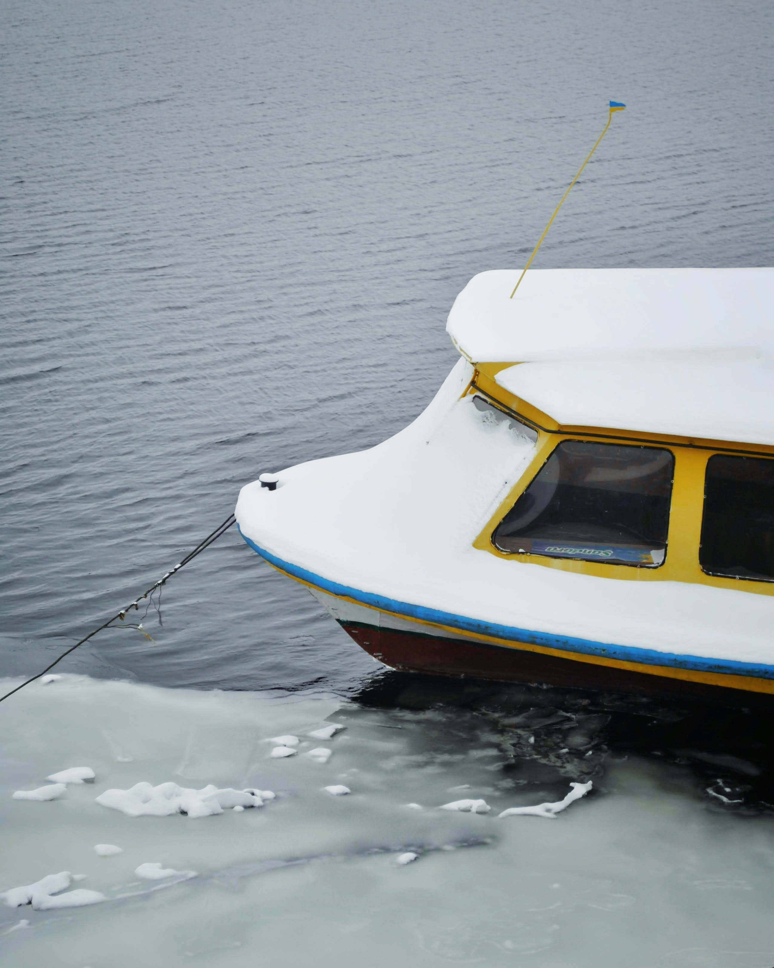Snow-Dusted Hull: A Yellow Cabin Boat Anchored by Ice-Fringed Waters