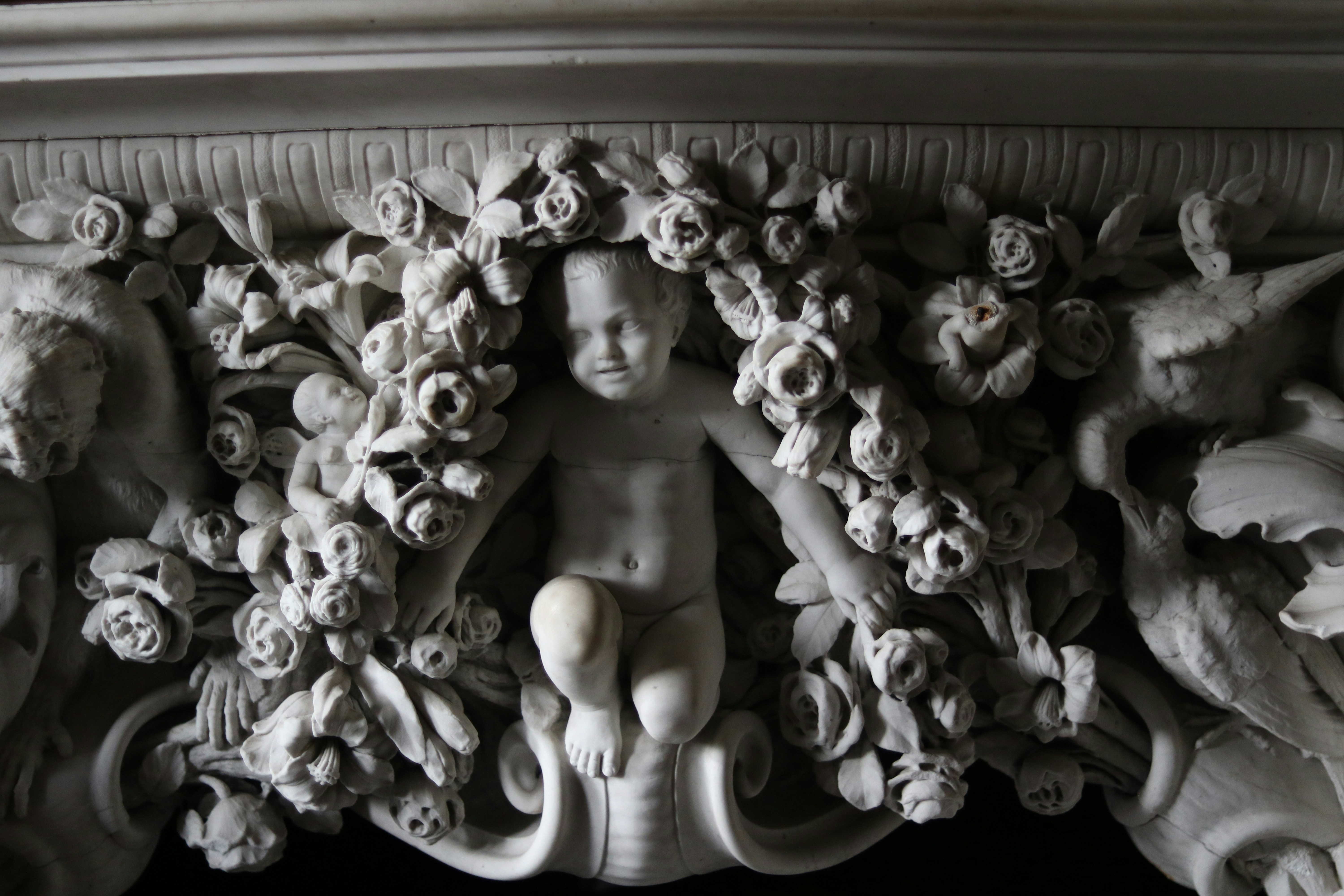 Intricate marble relief featuring a cherub nestled among roses, showcasing exquisite craftsmanship and detail.