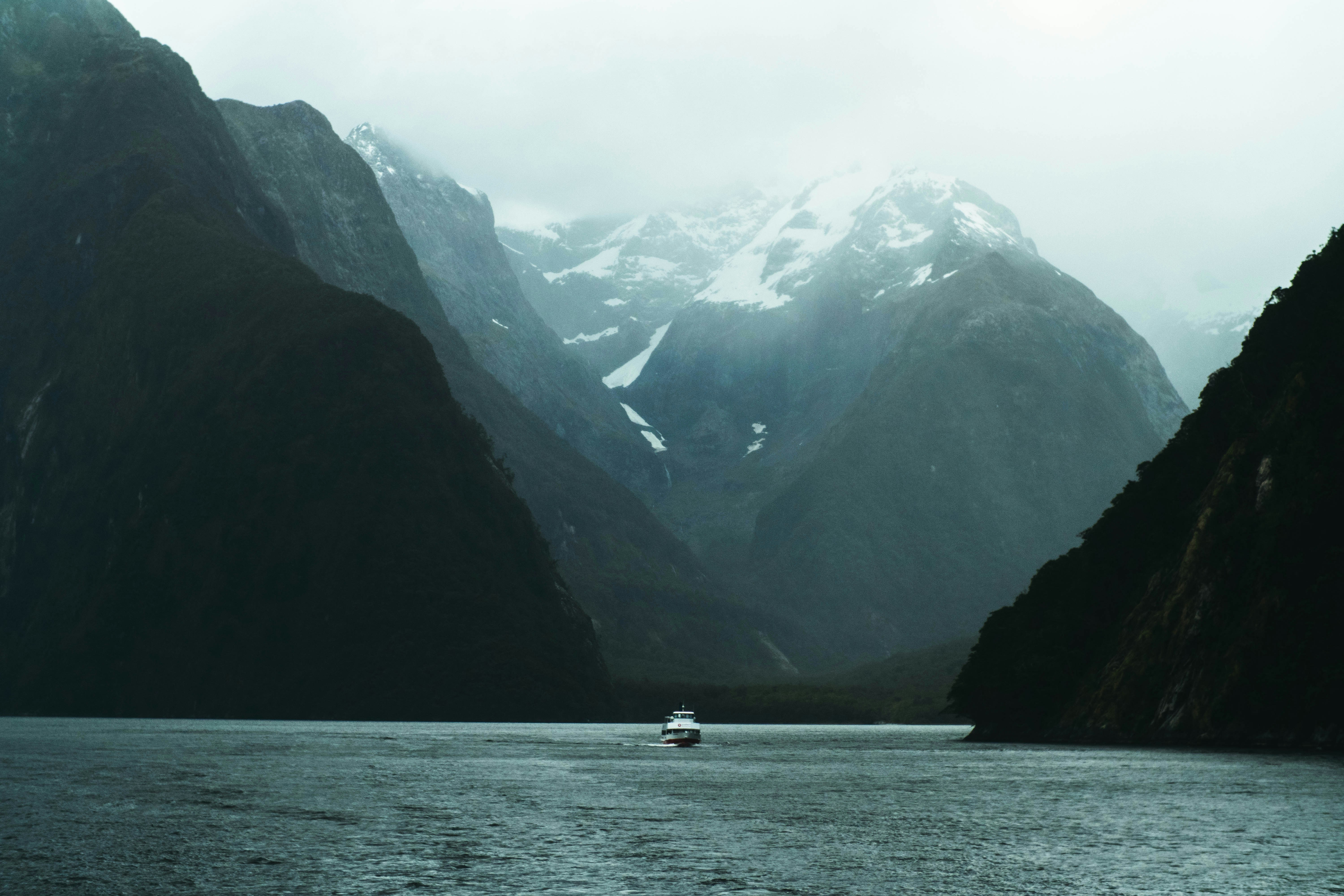 A solitary boat navigates through a serene fjord, surrounded by towering mountains shrouded in mist. The scene evokes a sense of adventure and tranquility.