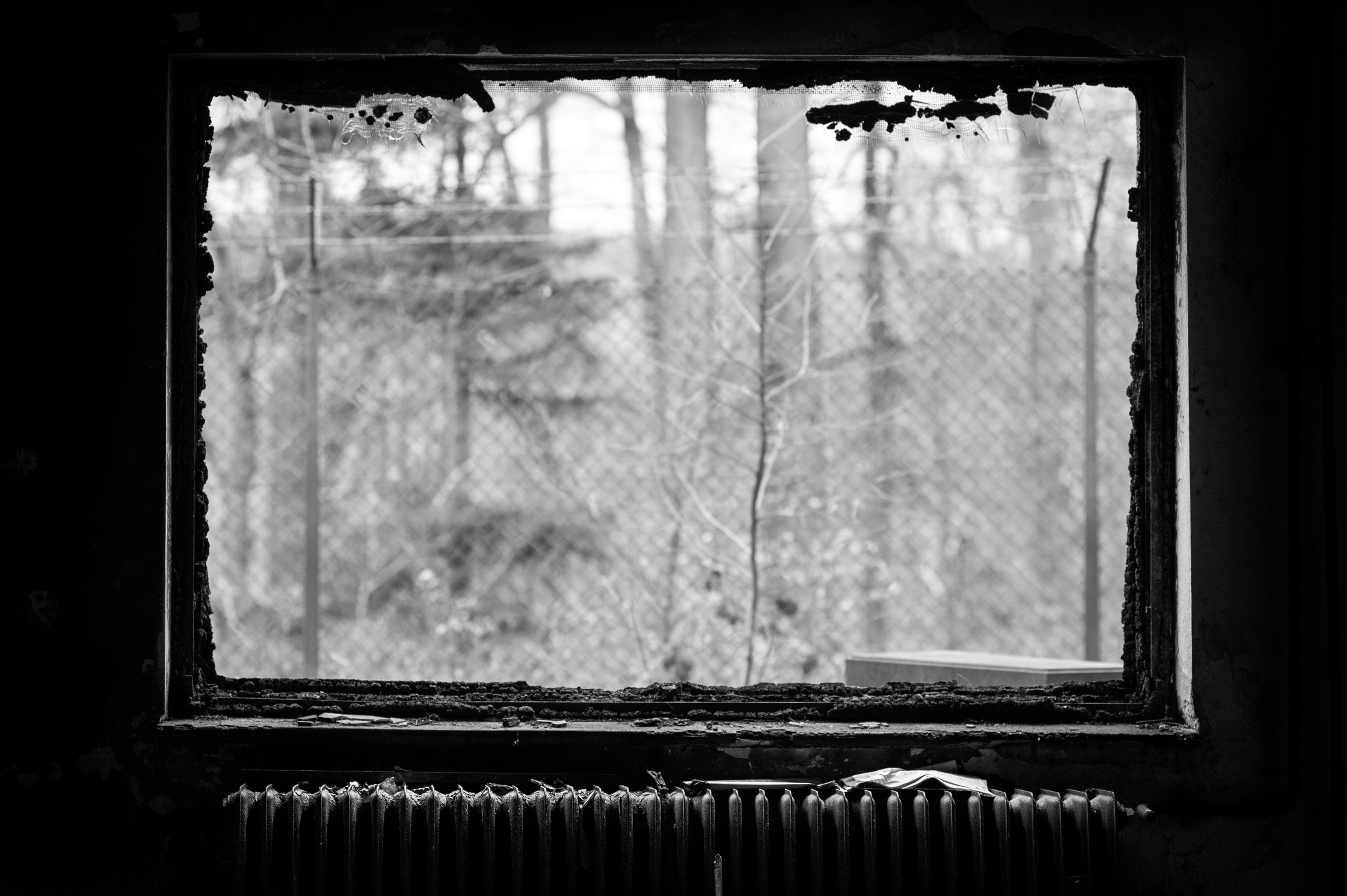 Rustic window frame revealing a blurred view of a desolate outdoor landscape behind a chain-link fence.