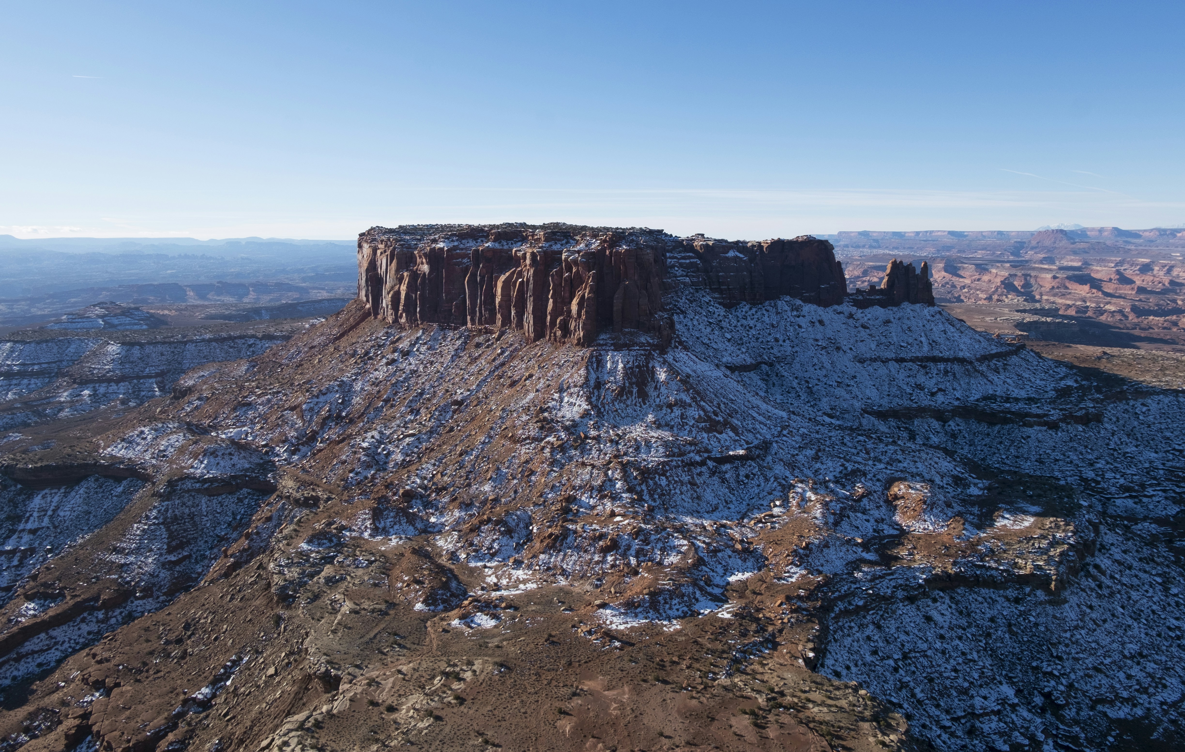 Snow-dusted mesa under a clear blue sky in a vast desert landscape.