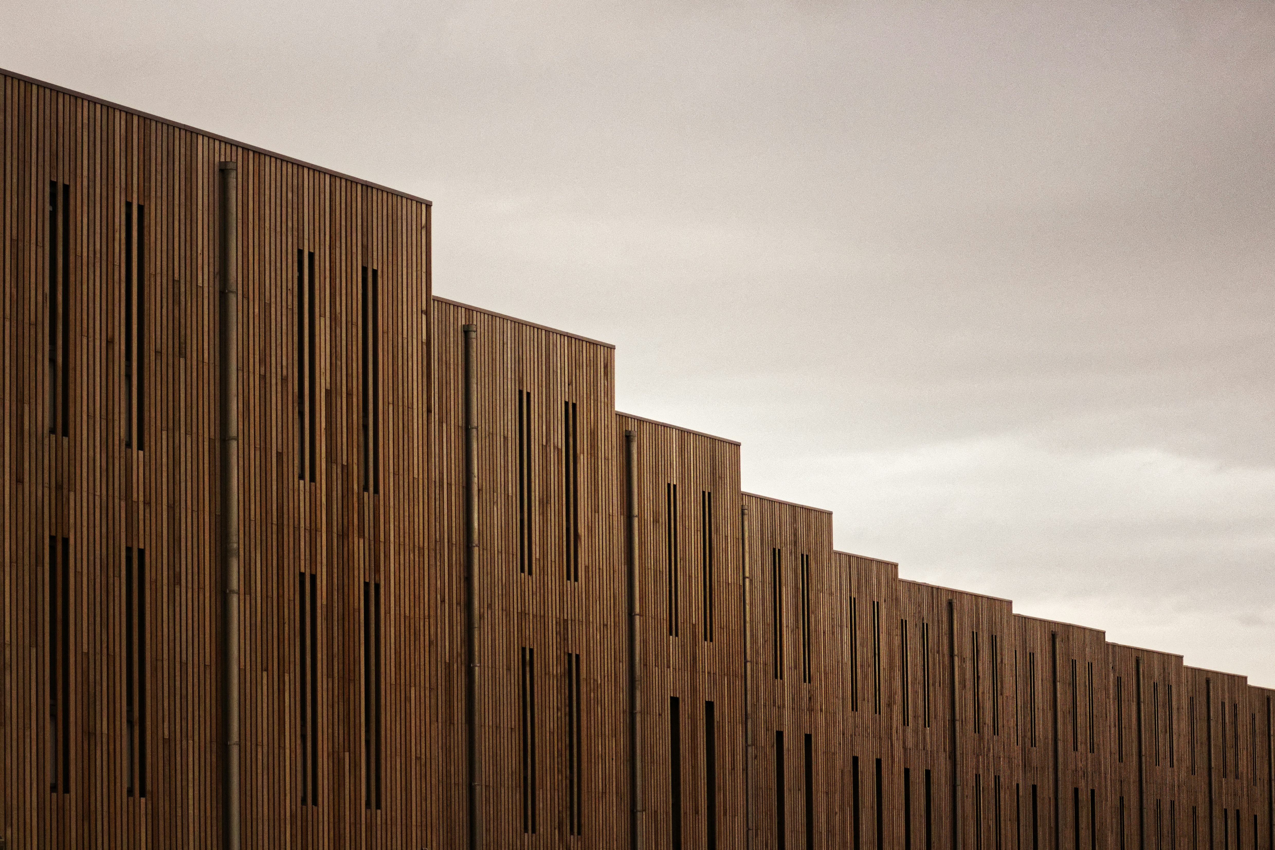 Contemporary wooden building facade with vertical slats against a cloudy sky, showcasing modern architectural design.