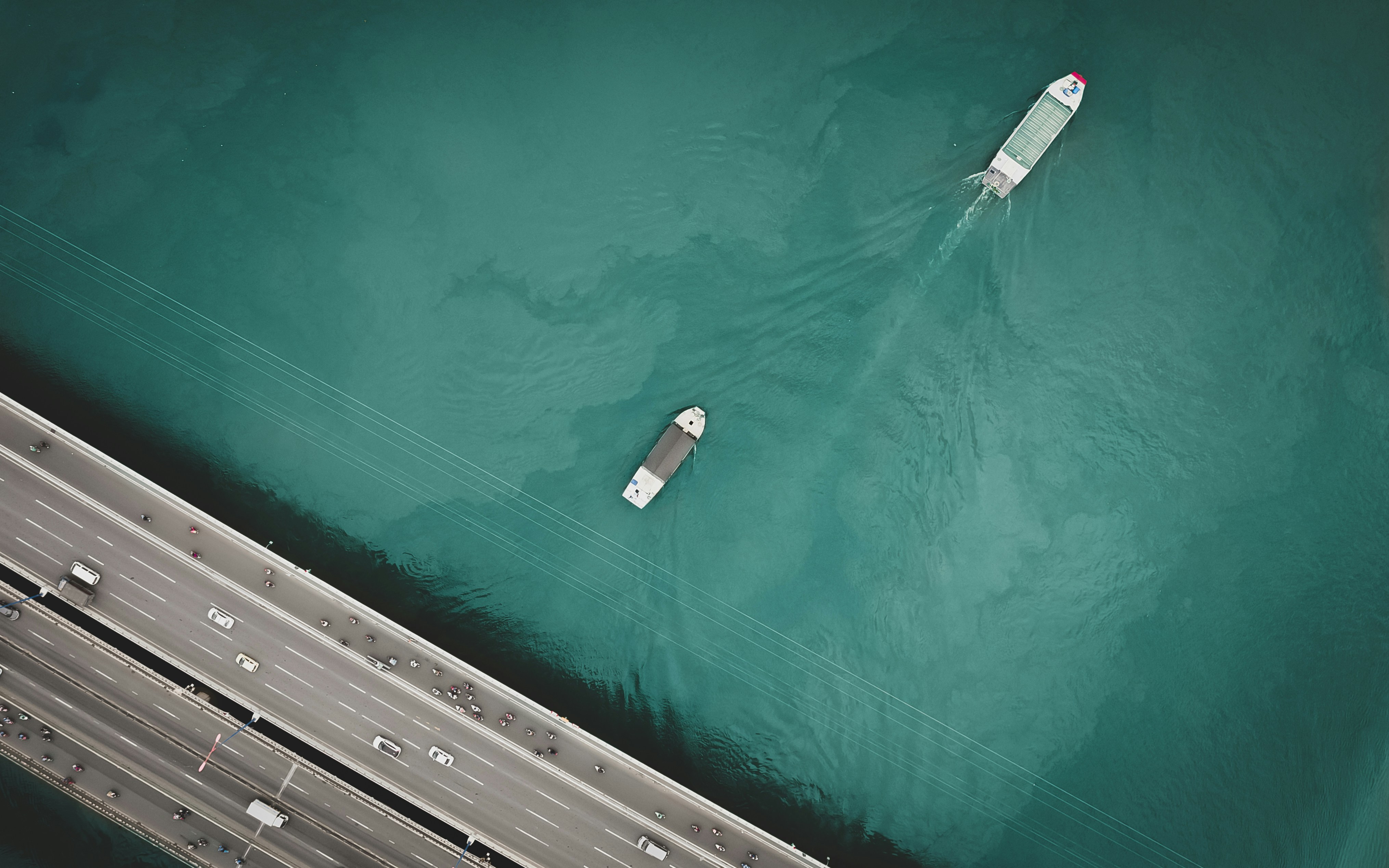 Two boats navigate the tranquil waters beside a busy highway, showcasing the contrast between nature and urban life.