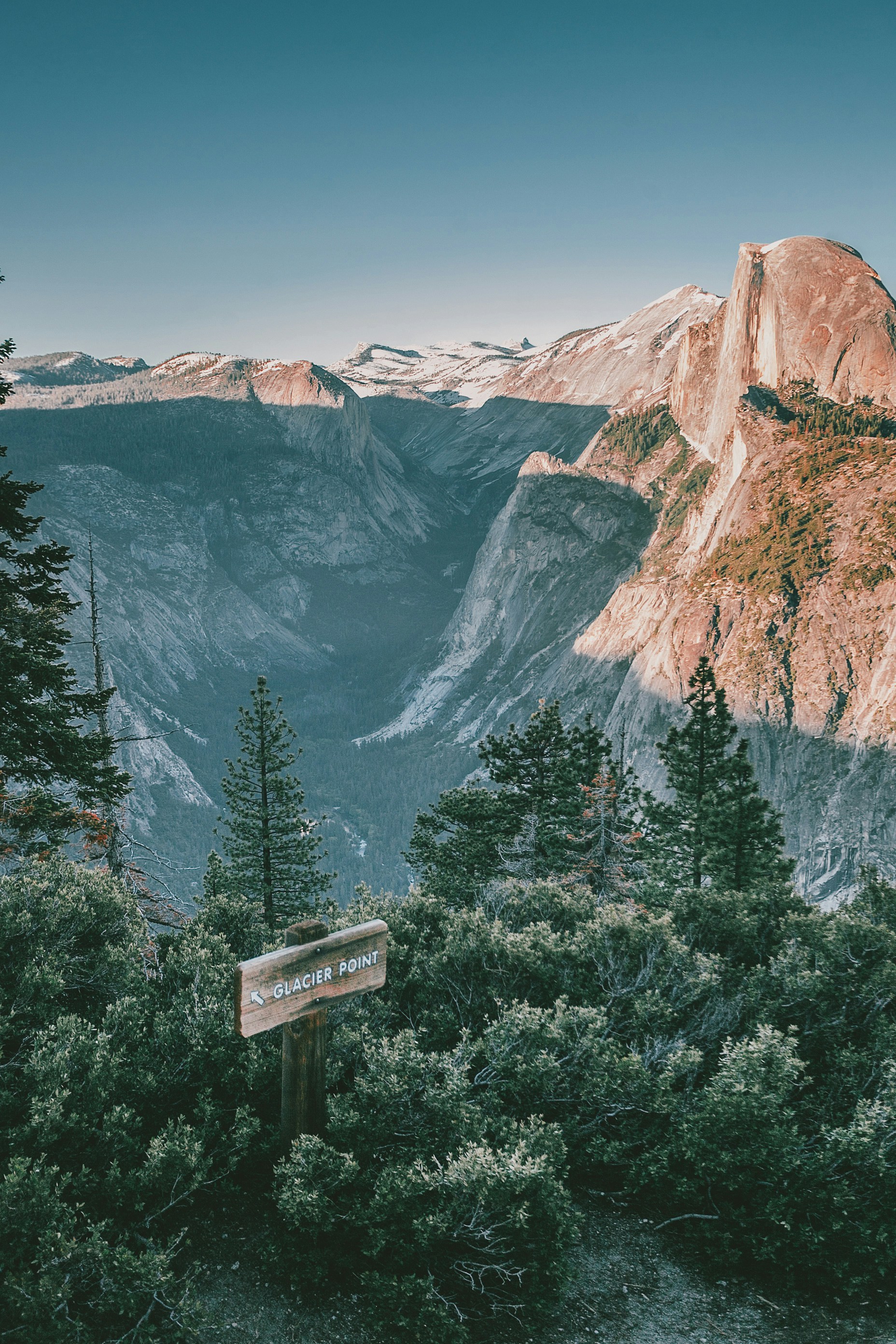 A scenic view from Glacier Point showcasing the dramatic cliffs and valleys of Yosemite National Park, with a wooden sign marking the location.
