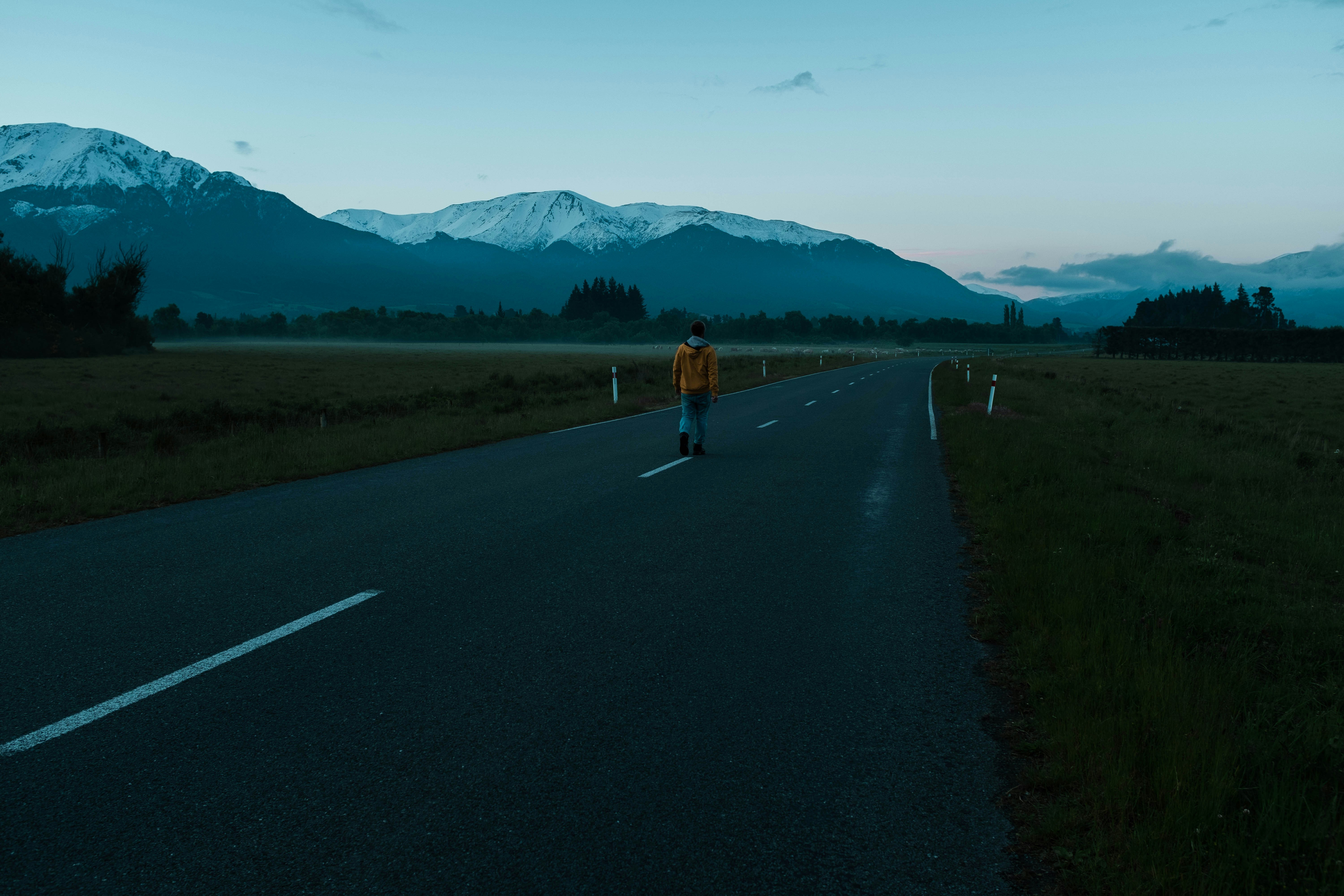 Lone Traveler on a Quiet Road Beneath Snowy Peaks at Blue Hour