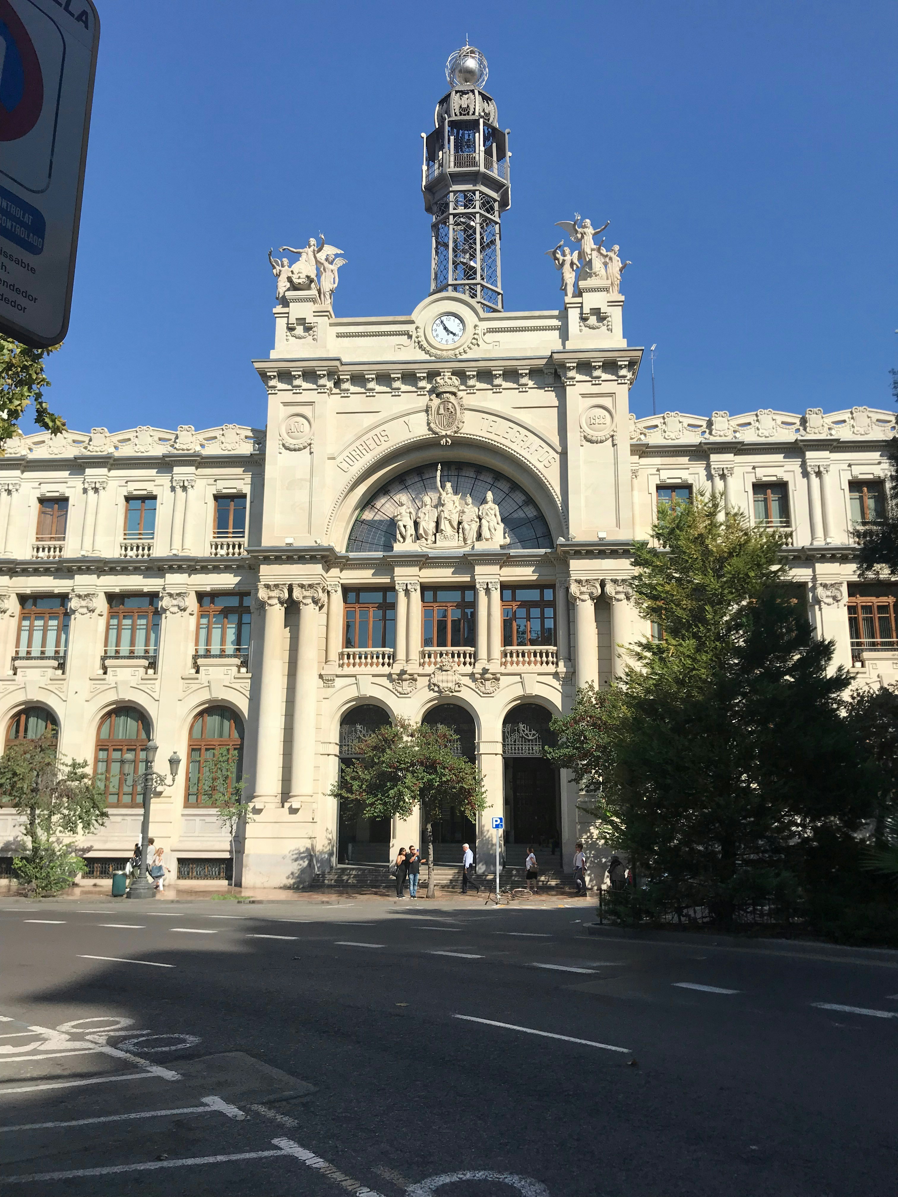 Imposing historical building featuring intricate architectural details and a prominent clock tower against a clear blue sky.