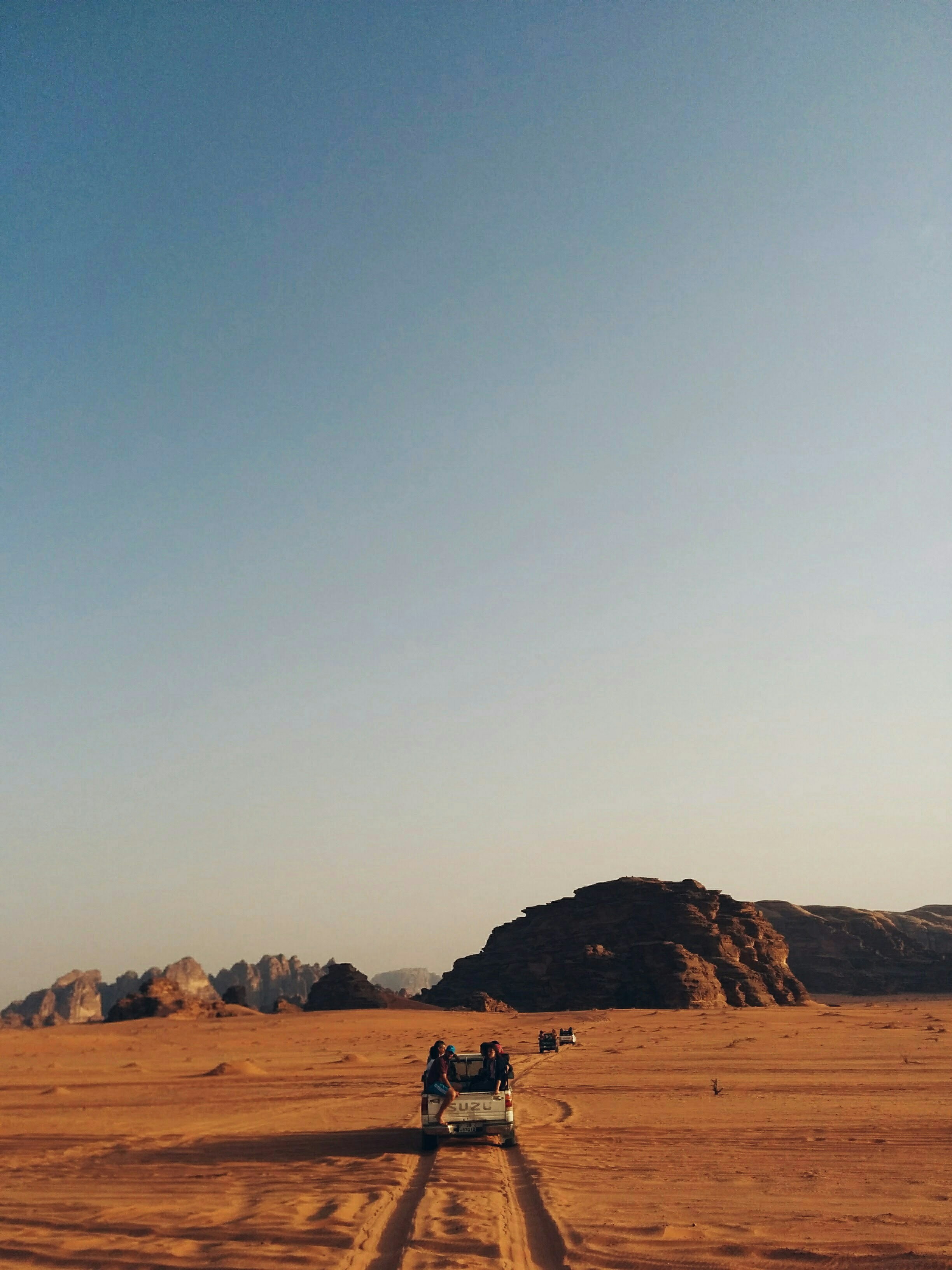 Off-road vehicle traversing the vast desert landscape with rocky formations in the background under a clear sky.