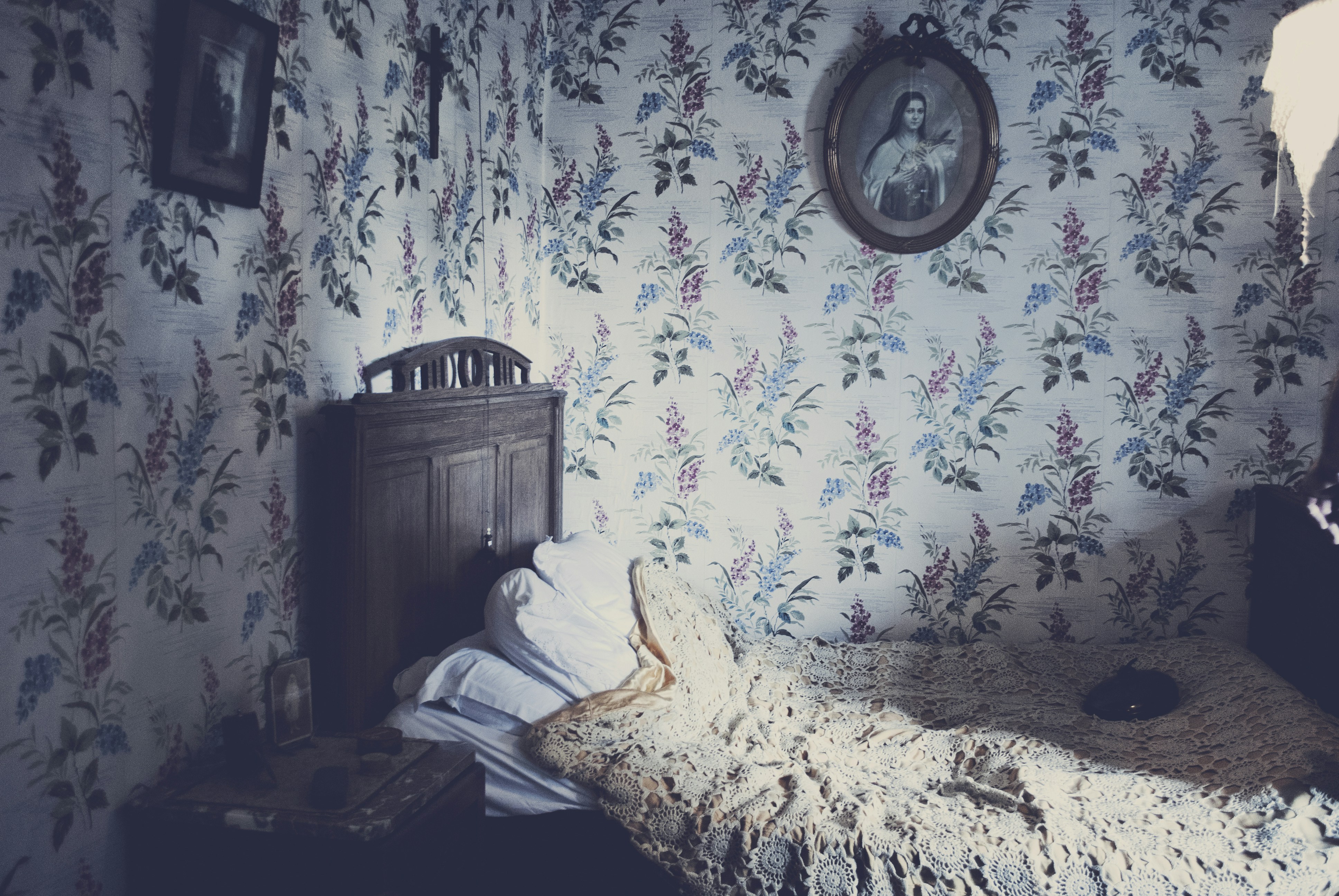 Cozy bedroom adorned with floral wallpaper, featuring a vintage bed and a portrait hanging on the wall. The scene evokes nostalgia and tranquility.