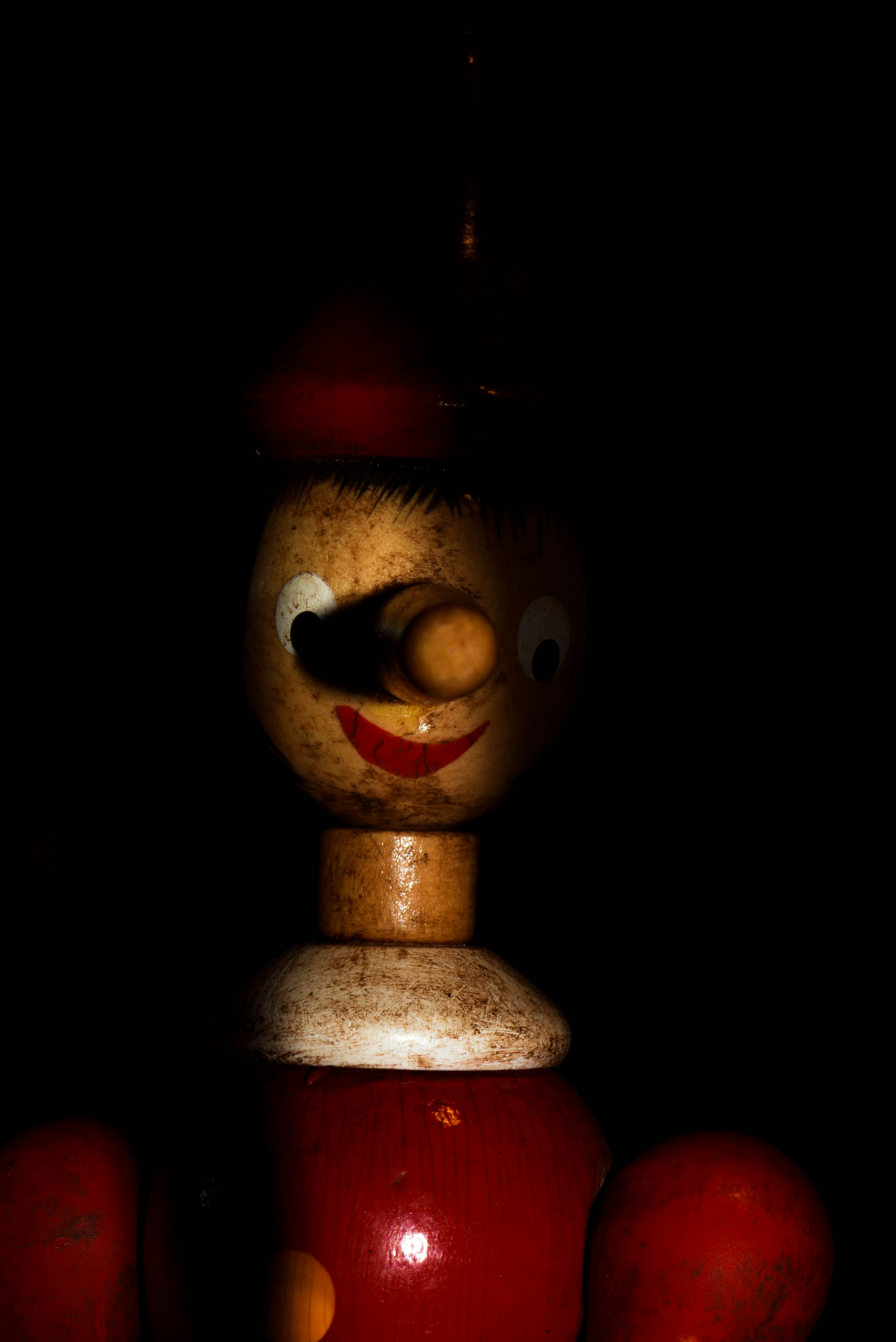 Wooden puppet with a cheerful expression partially illuminated against a dark background, evoking a sense of nostalgia.