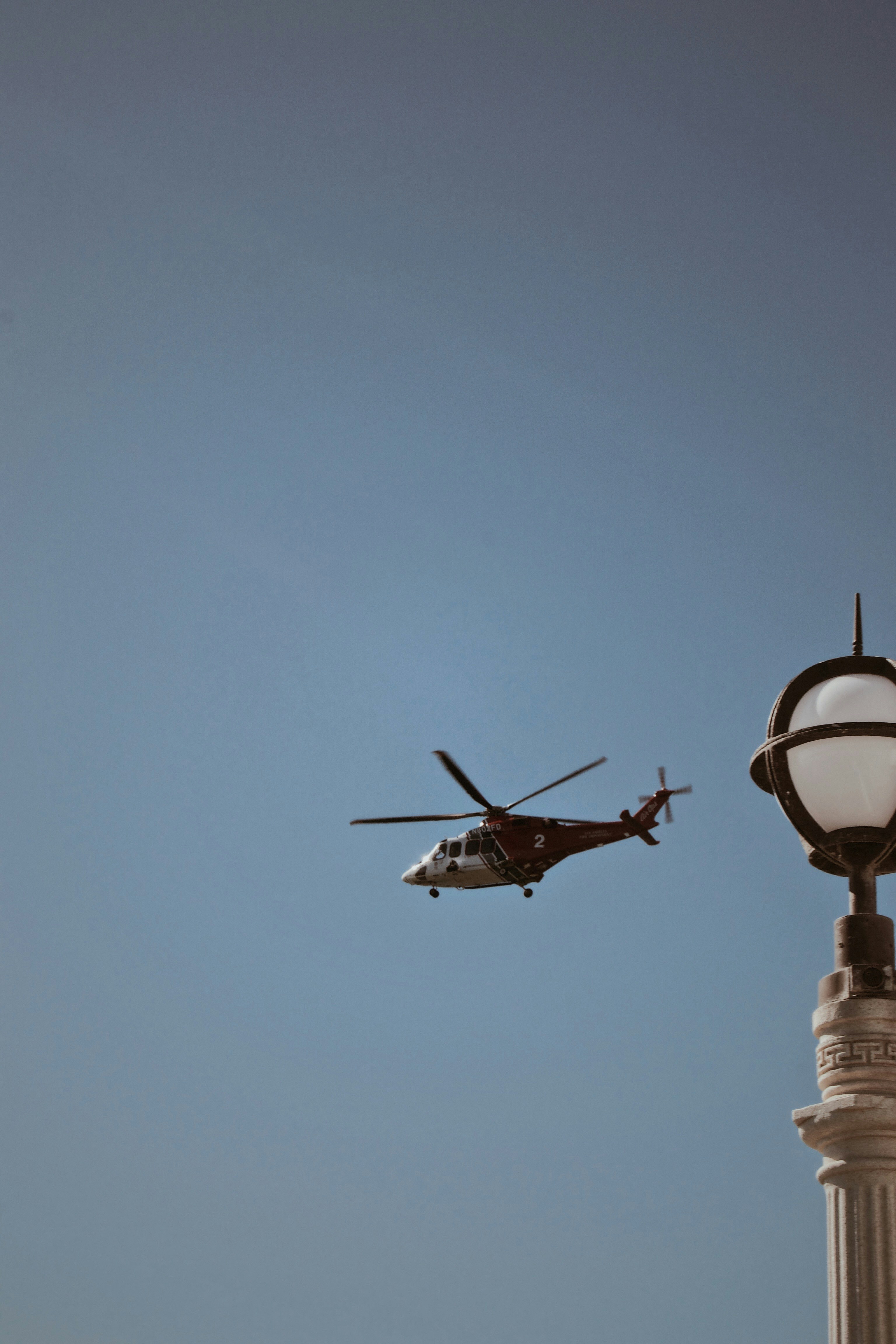 Aerial Escort: helicopter passing a decorative lamp against a pale sky