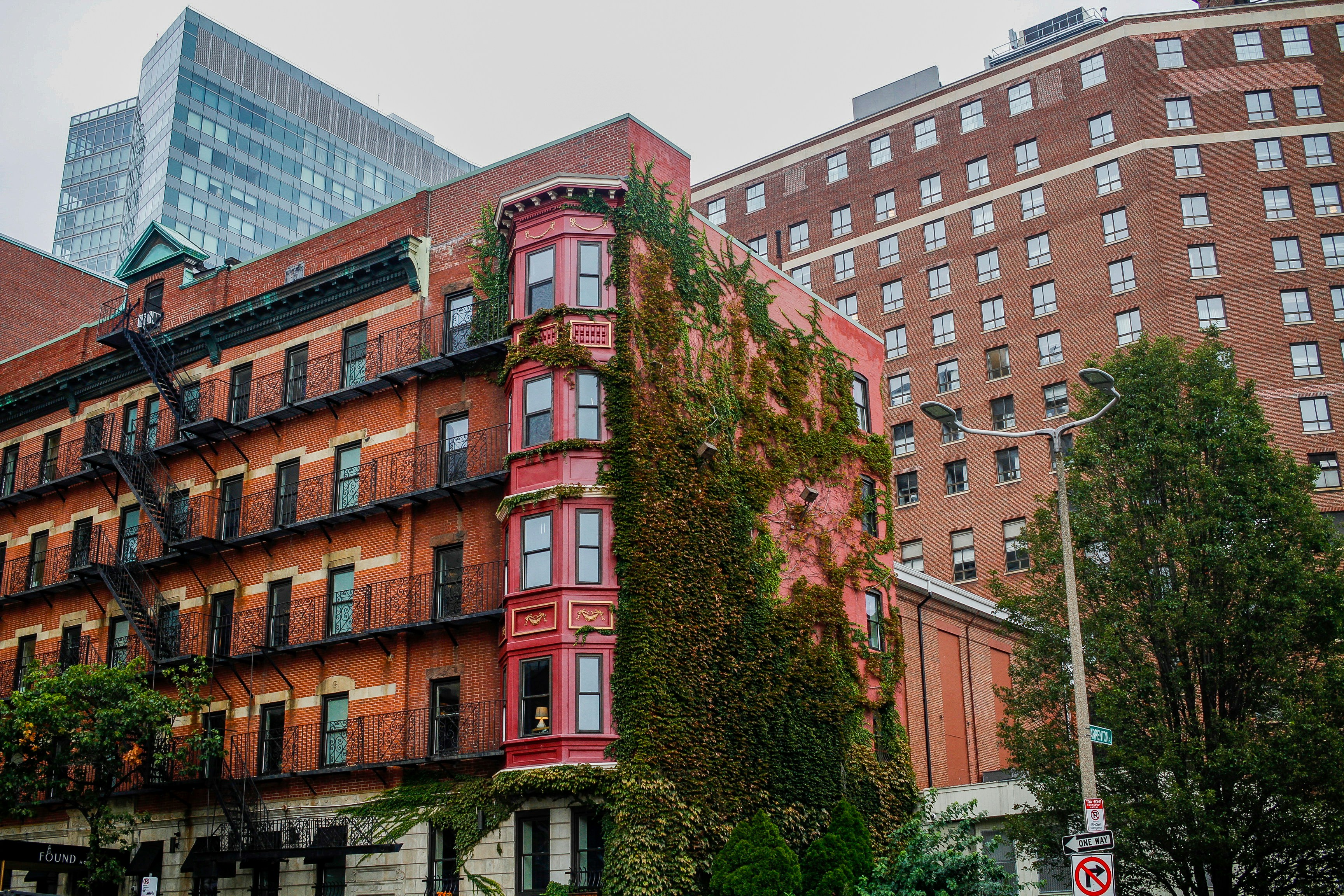 Red brick buildings with ivy alongside a modern glass tower under an overcast sky.