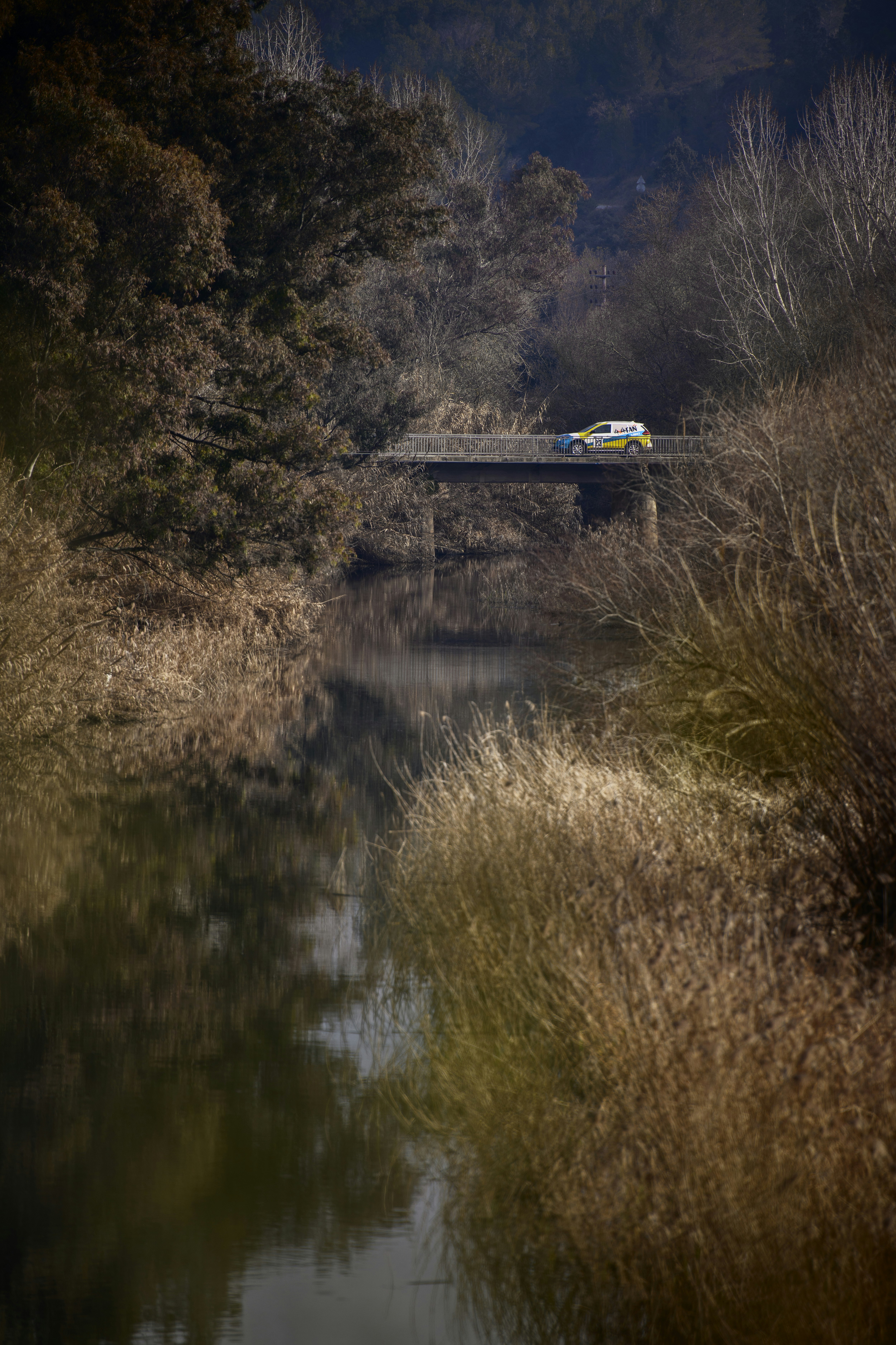 Crossing in Solitude: a yellow rally car on a quiet river bridge