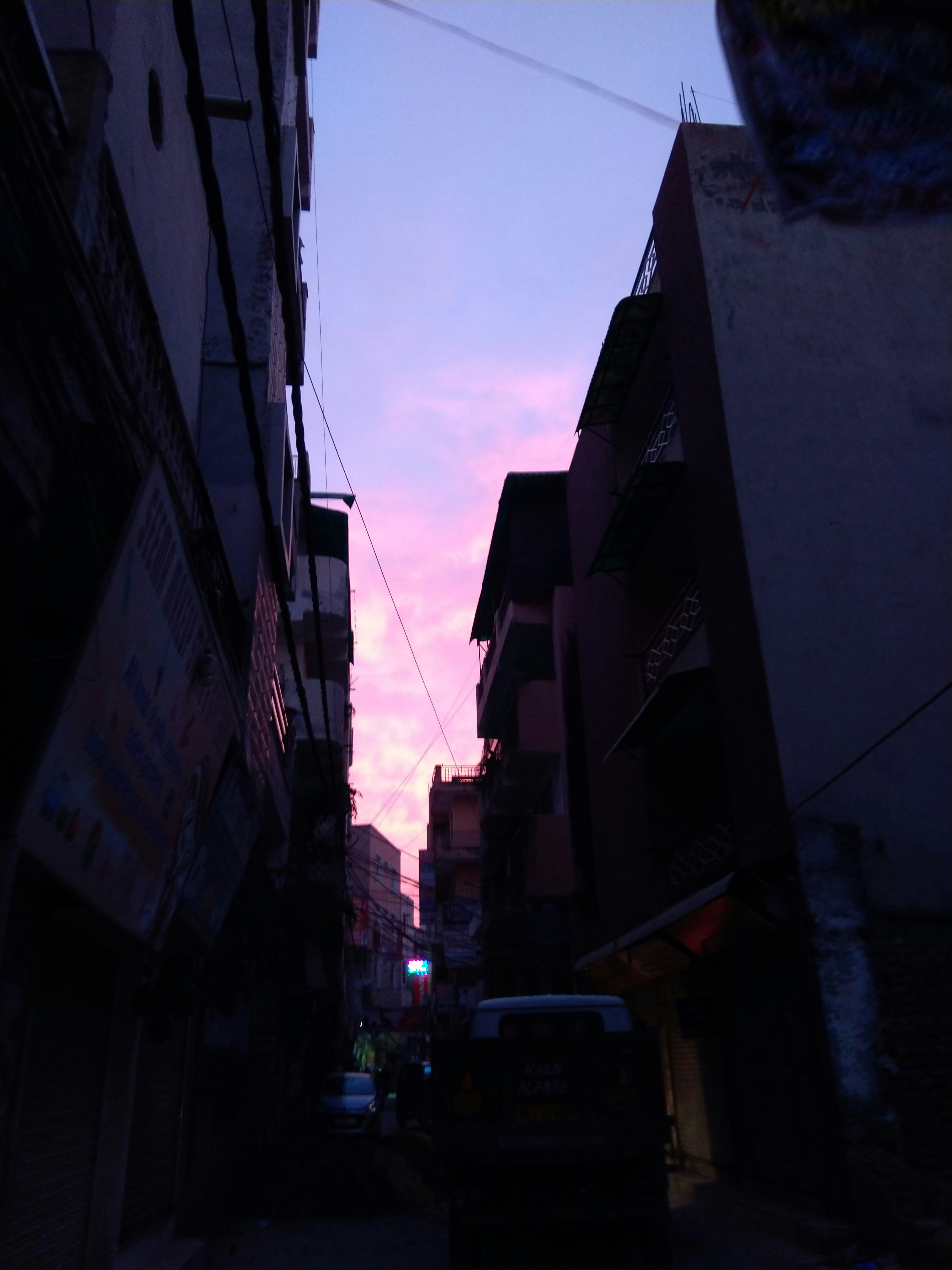 Narrow alleyway framed by buildings, with a vibrant pink sky peeking through at dusk.