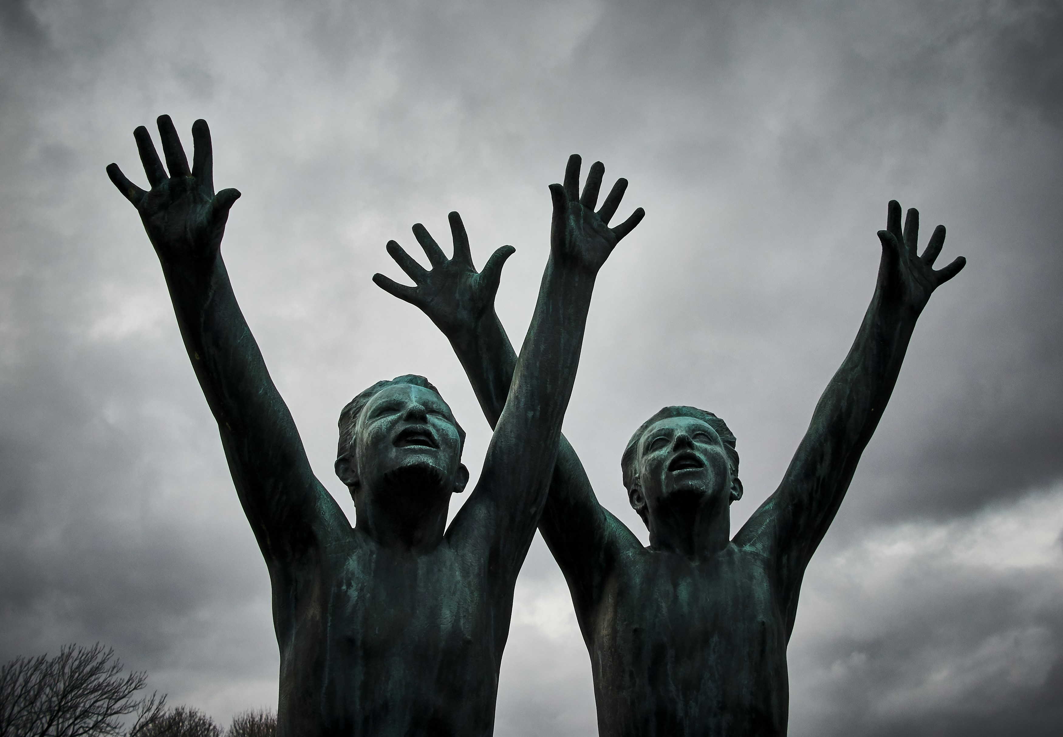 Two statues with raised arms beneath a dramatic, cloudy sky.