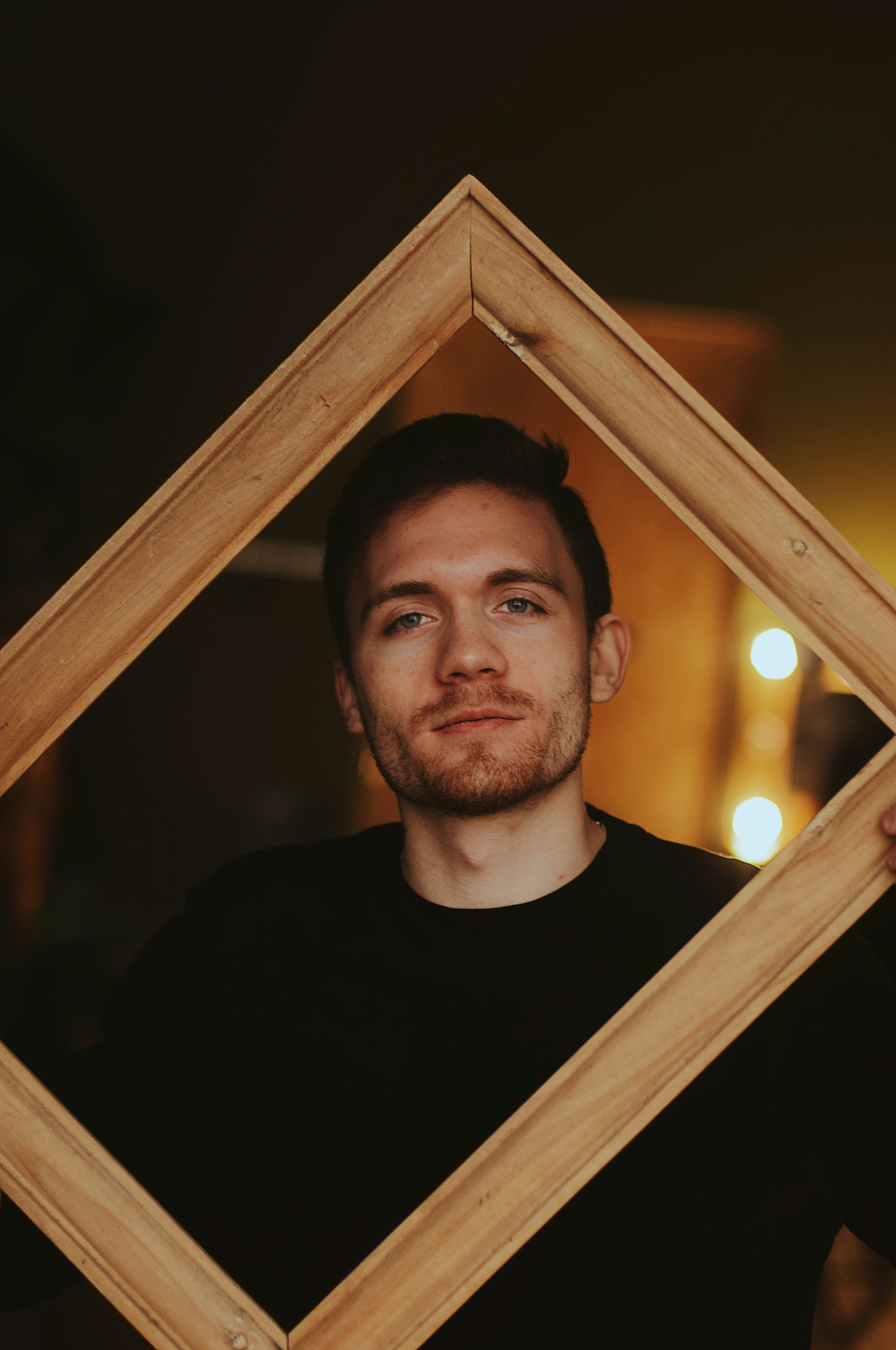 A young man holds a wooden frame in front of his face, creating a unique visual perspective that blends art and self-expression.