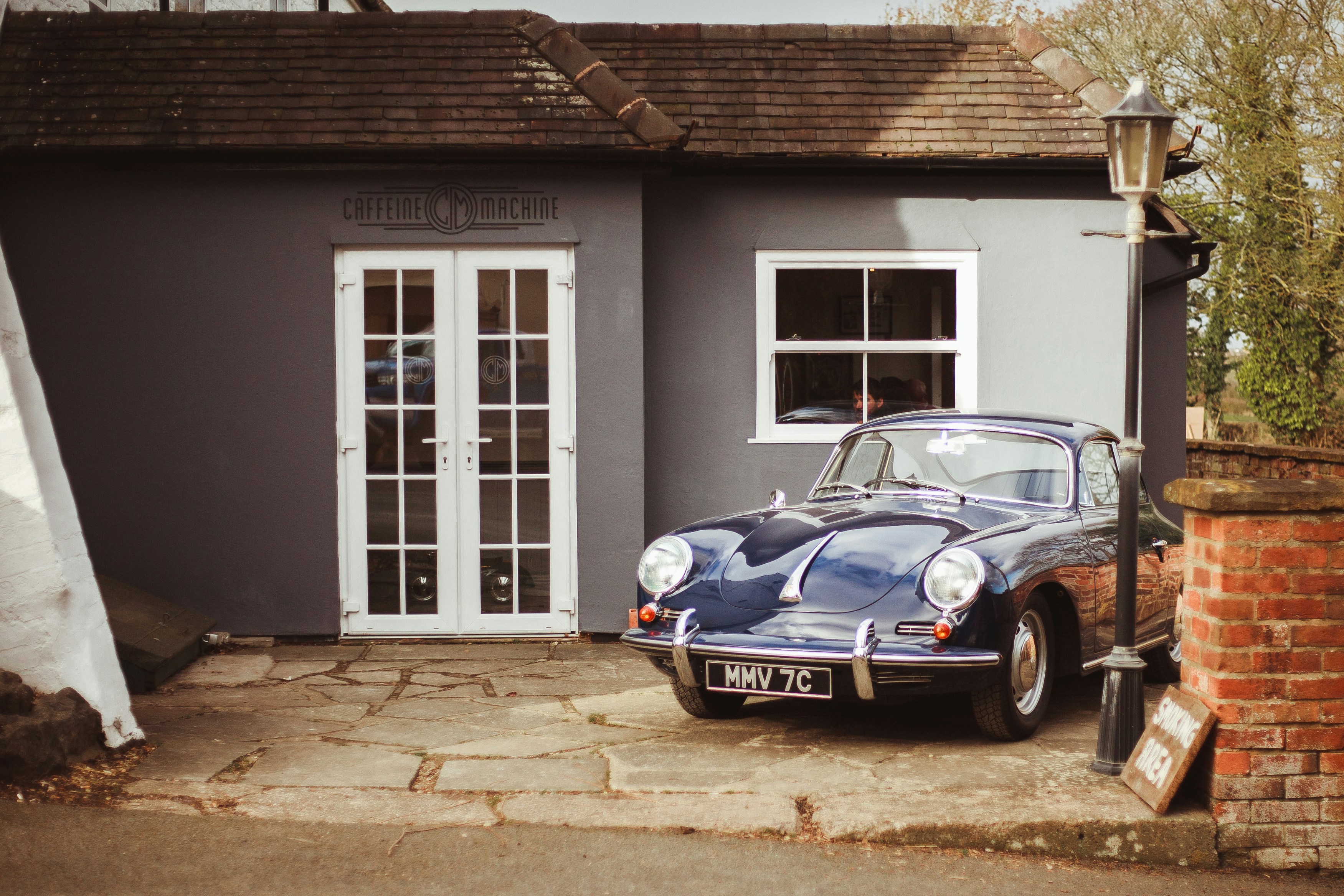 classic blue coupe parked beside gray and brown house