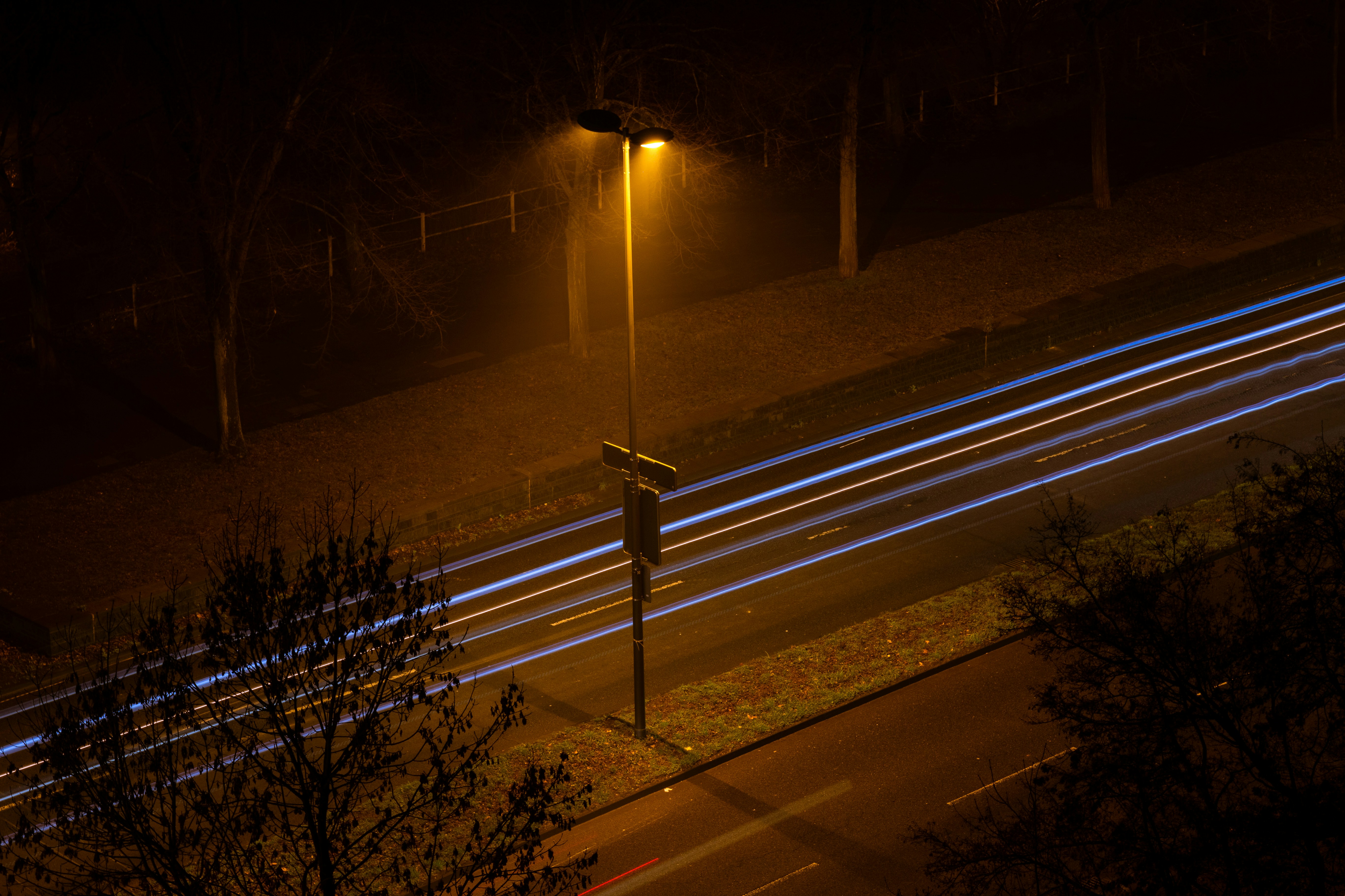 Long exposure captures the dynamic trails of vehicle lights on a foggy street, illuminated by a solitary streetlamp.