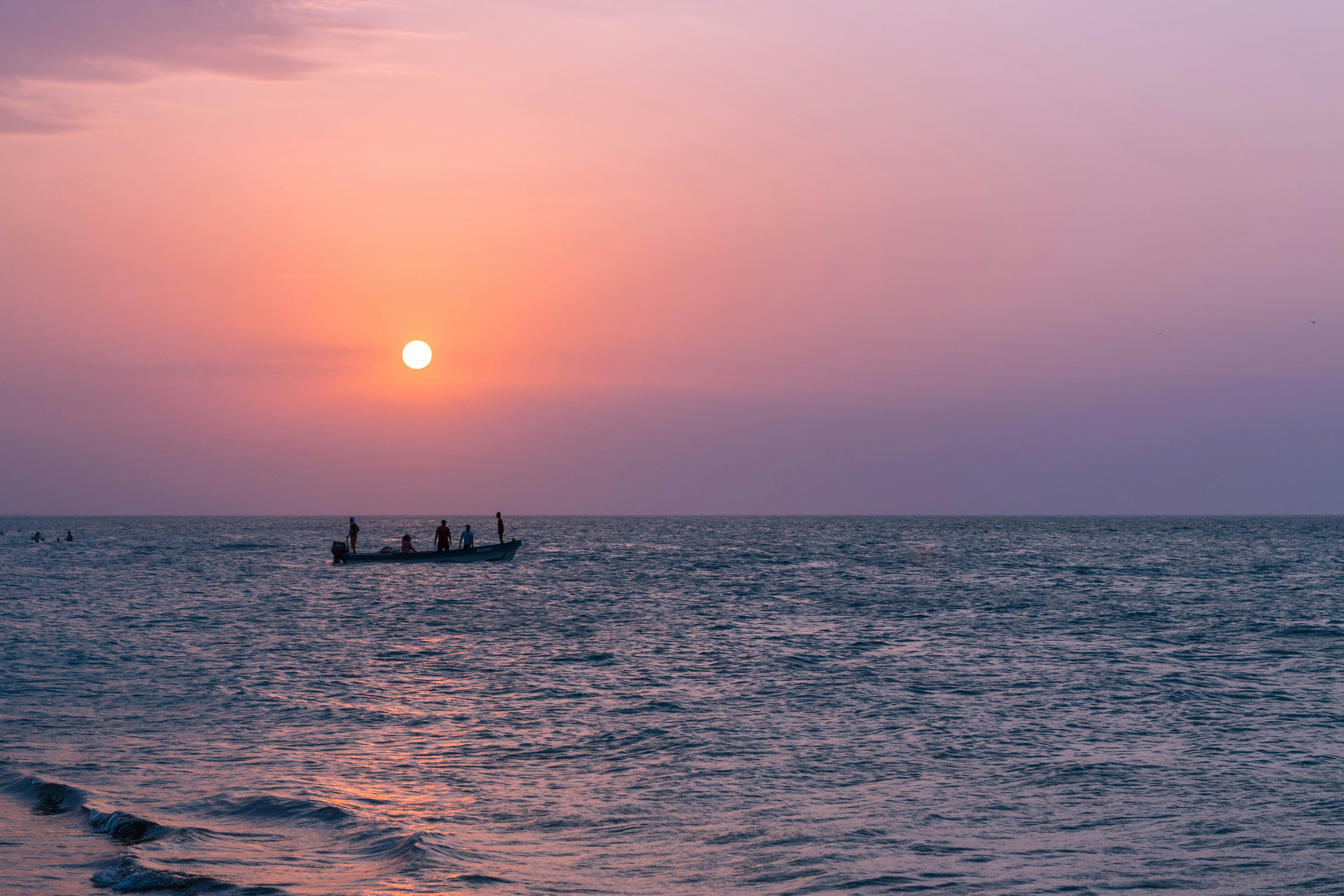 Silhouetted fishermen on a boat against a vibrant sunset over calm waters.