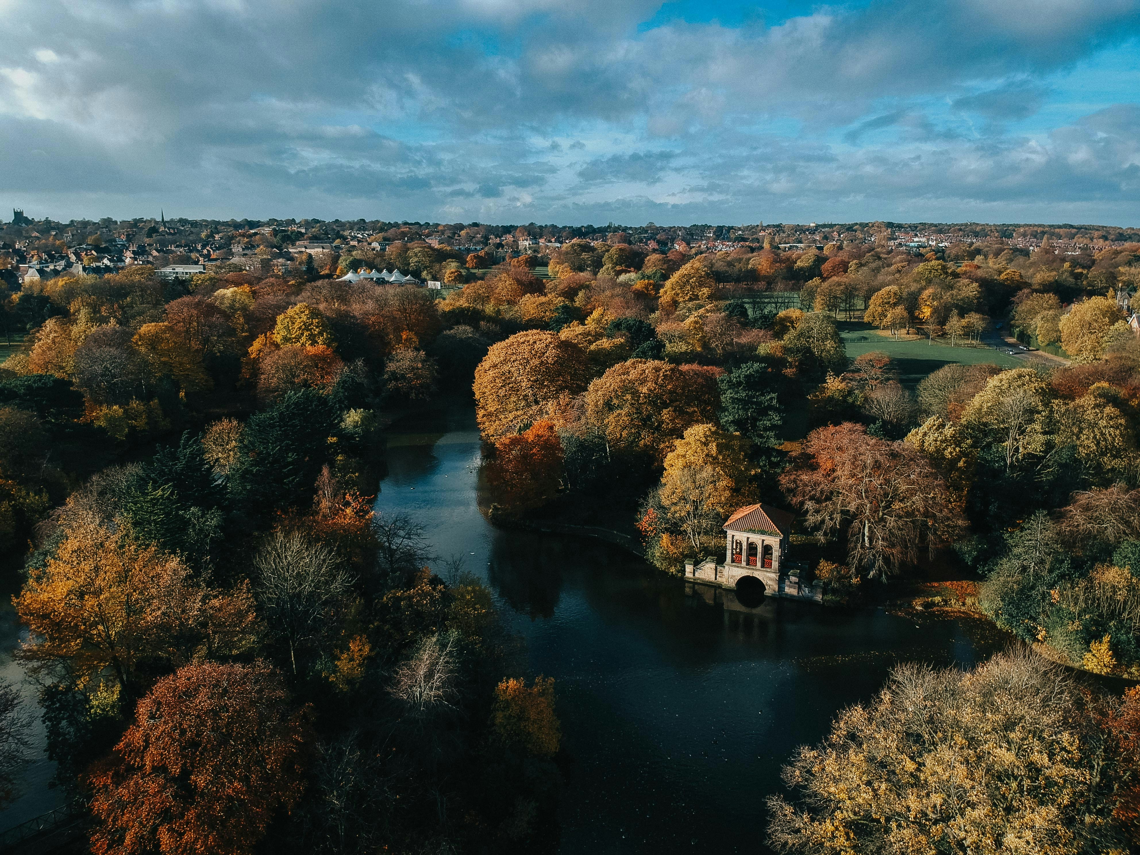 Aerial view of a serene lake surrounded by vibrant autumn foliage under a partly cloudy sky.