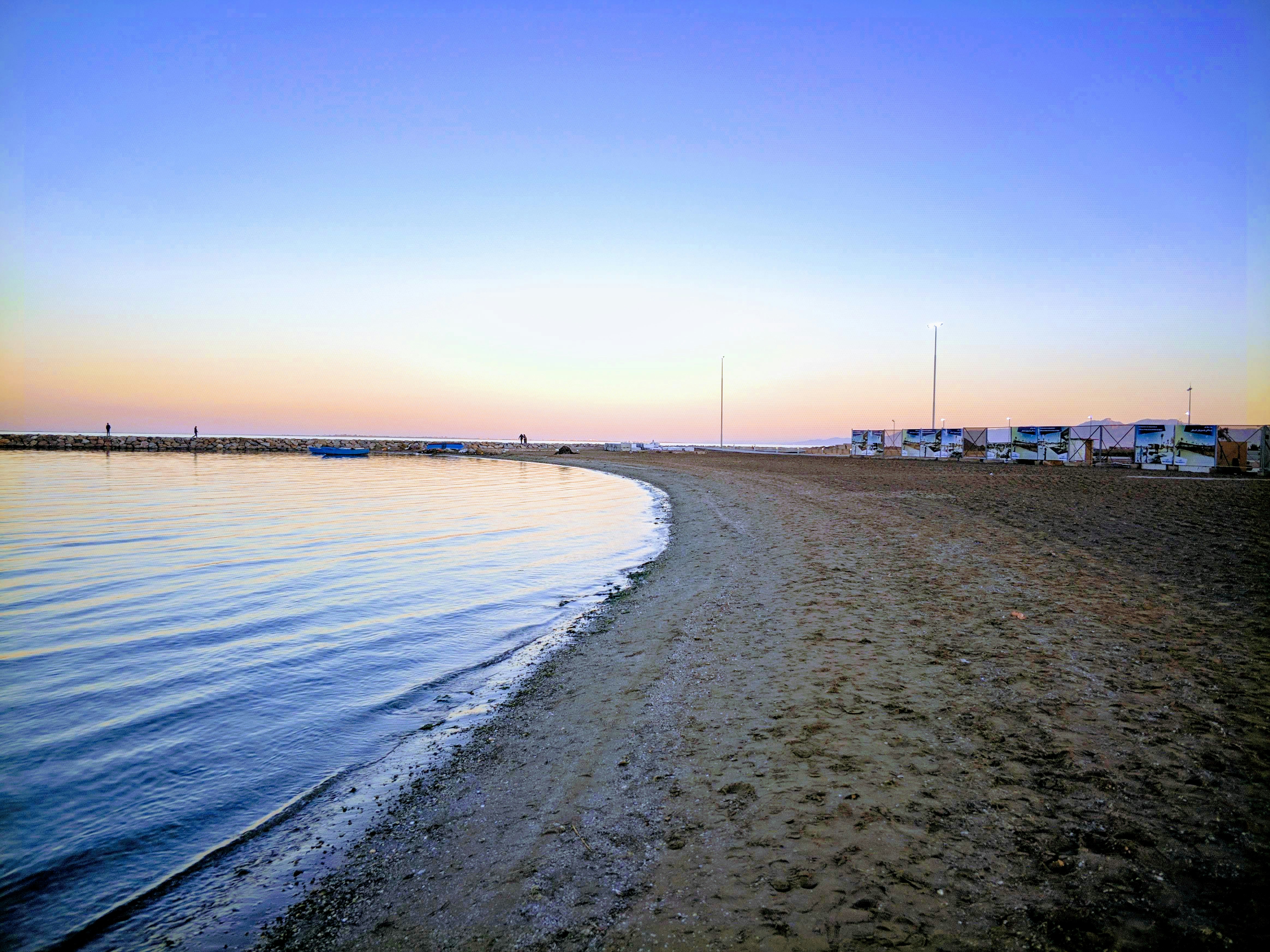 Curved shoreline meeting calm waters at dusk with a gradient sky transitioning from orange to blue.