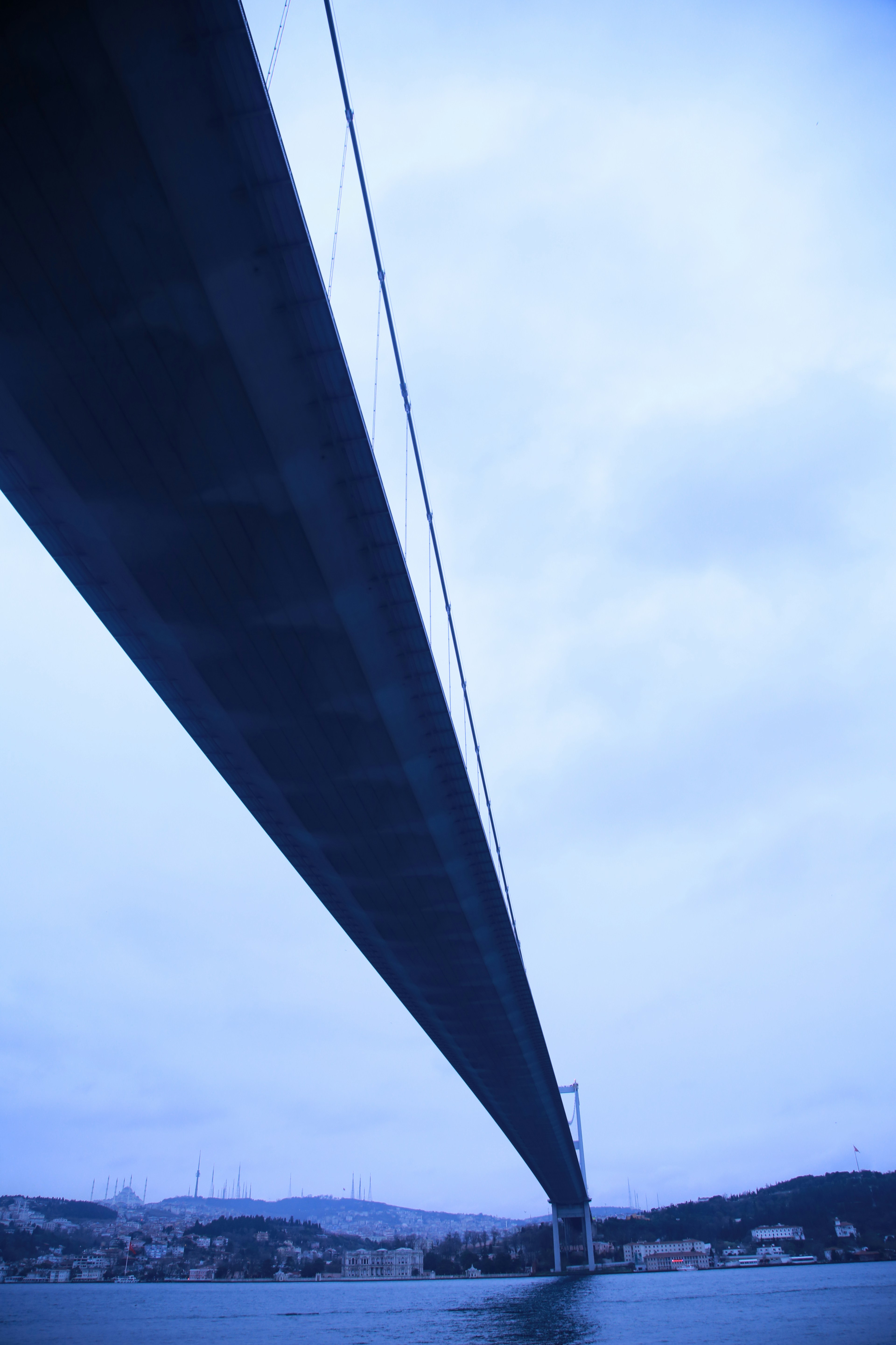 A dramatic view from beneath a large bridge, showcasing its architectural lines against a moody sky. The scene captures the interplay of structure and nature.
