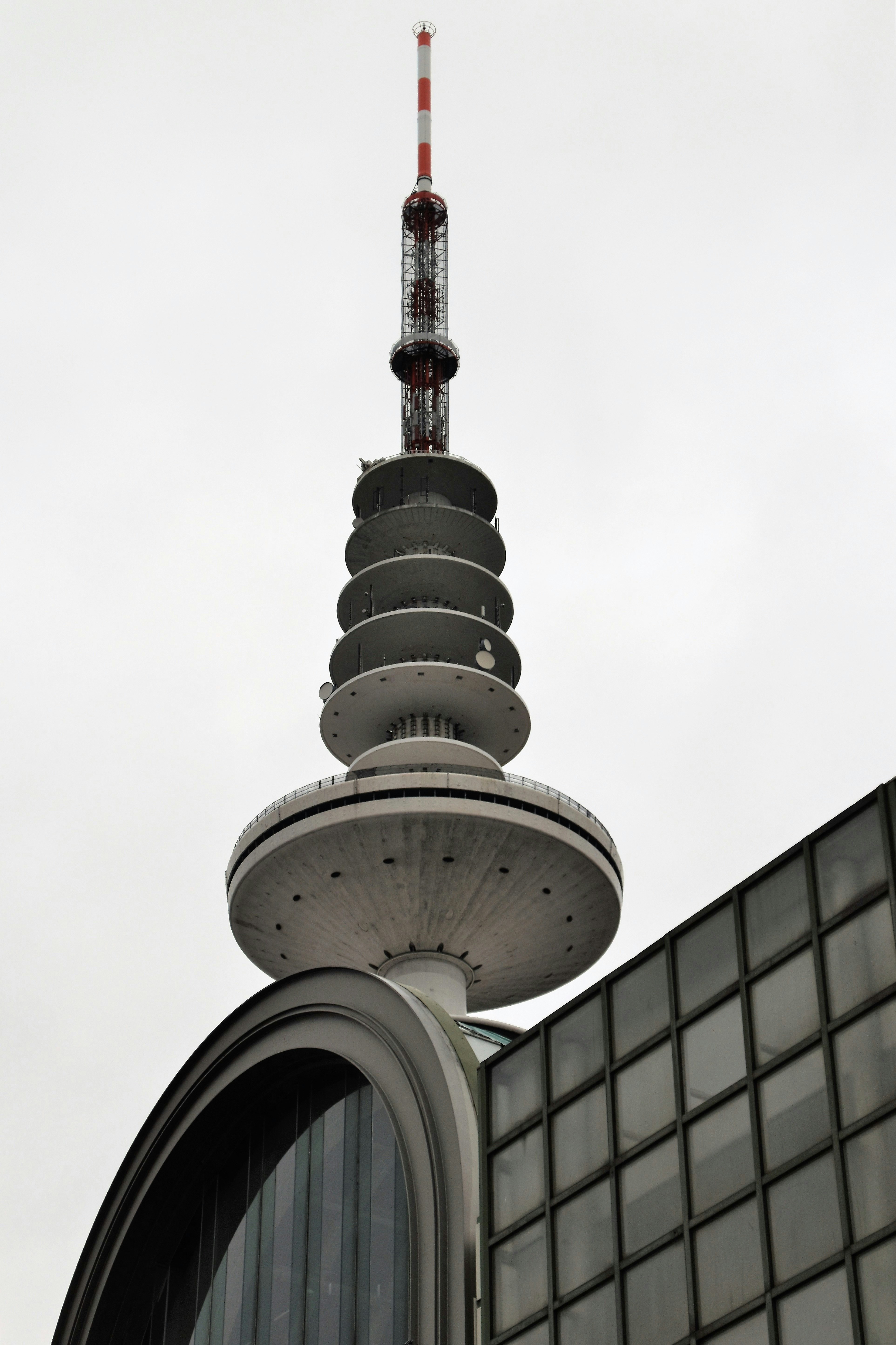 A modern communication tower rises above a sleek building, showcasing a blend of technology and design against a cloudy sky.