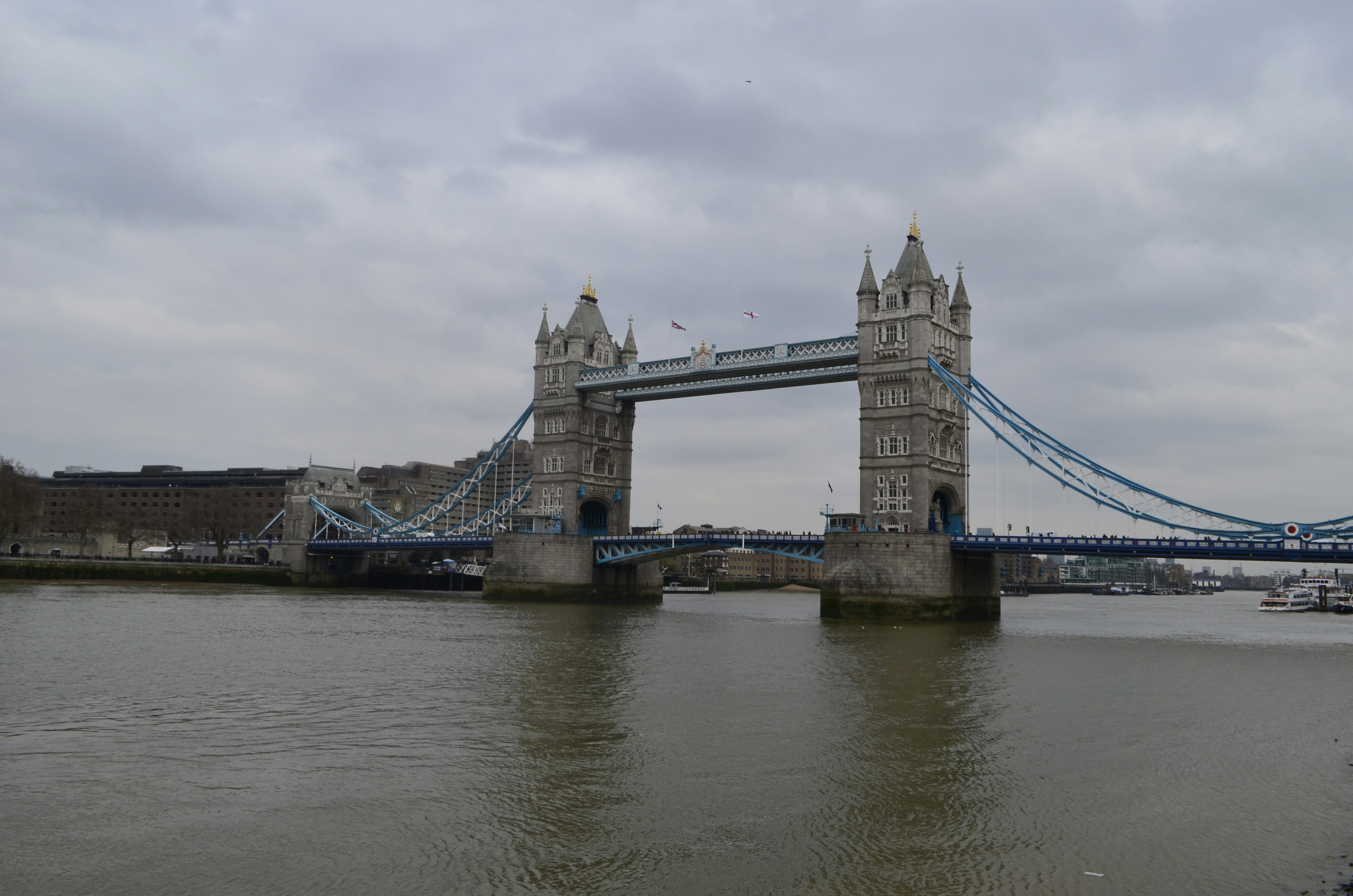Tower Bridge spans the River Thames, showcasing its iconic Victorian Gothic architecture under a cloudy sky.