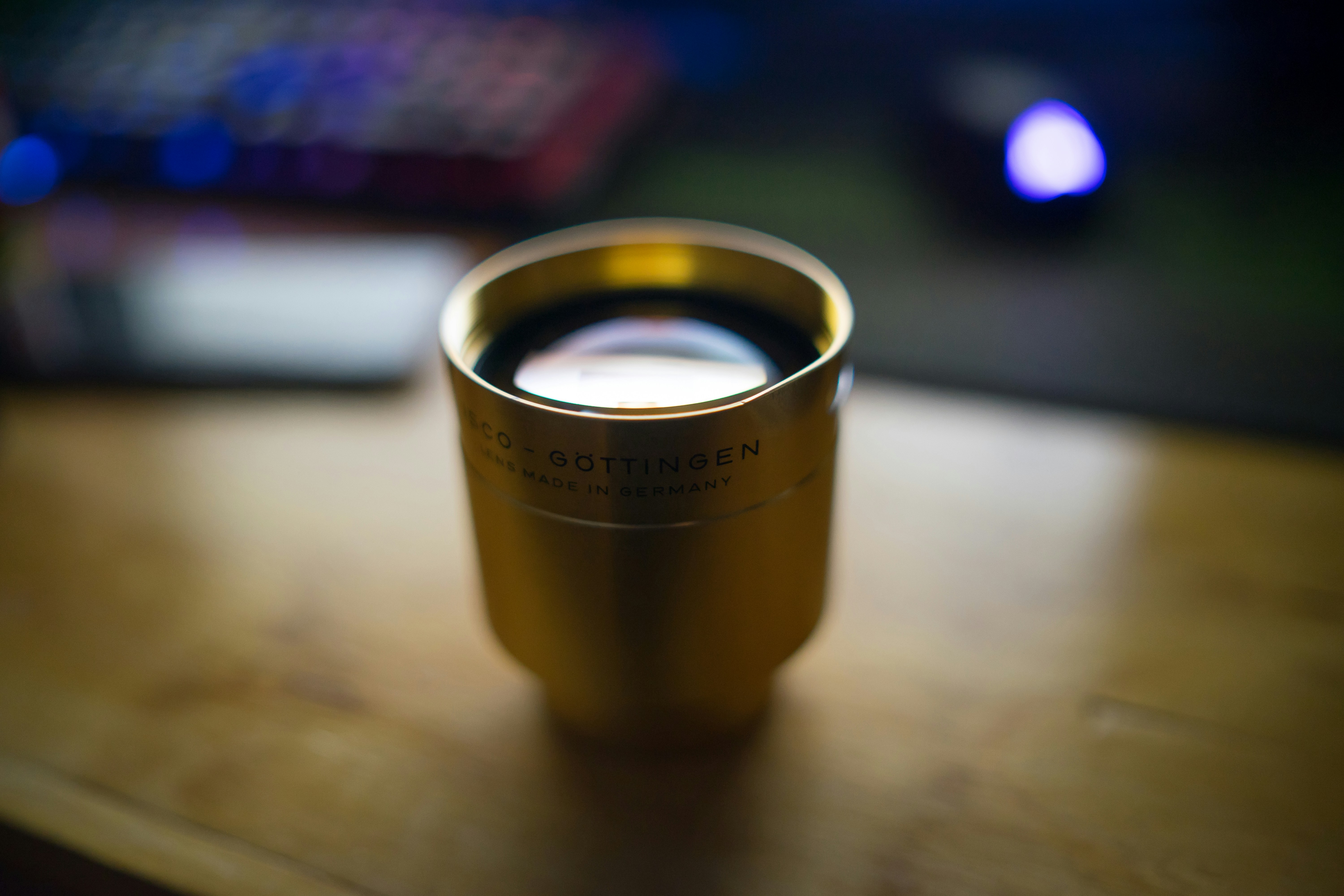 Golden Zeiss Lens on a Wooden Desk, Framed by Neon Blur