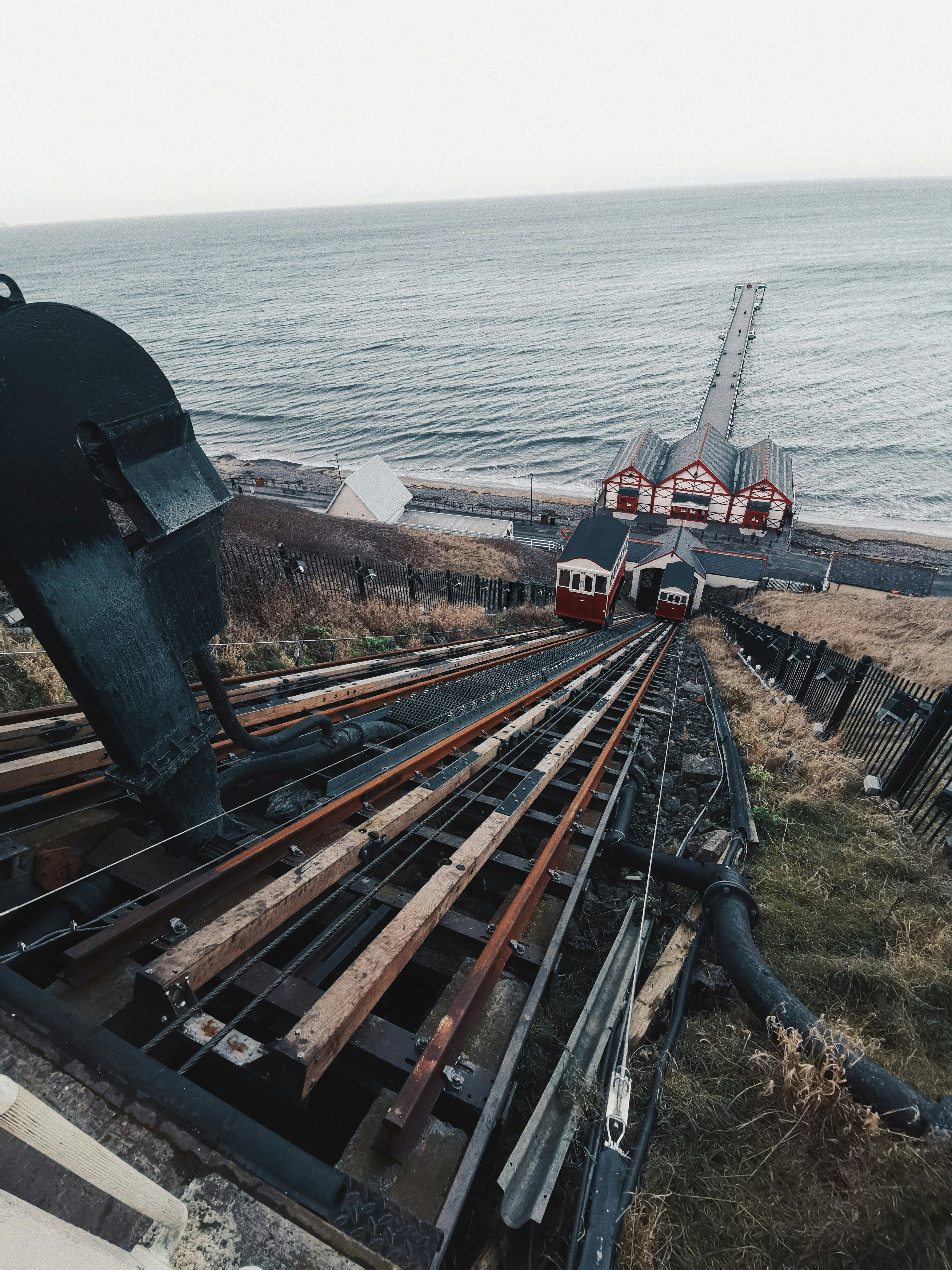 Steep railway tracks leading down to a coastal station by the sea under an overcast sky.