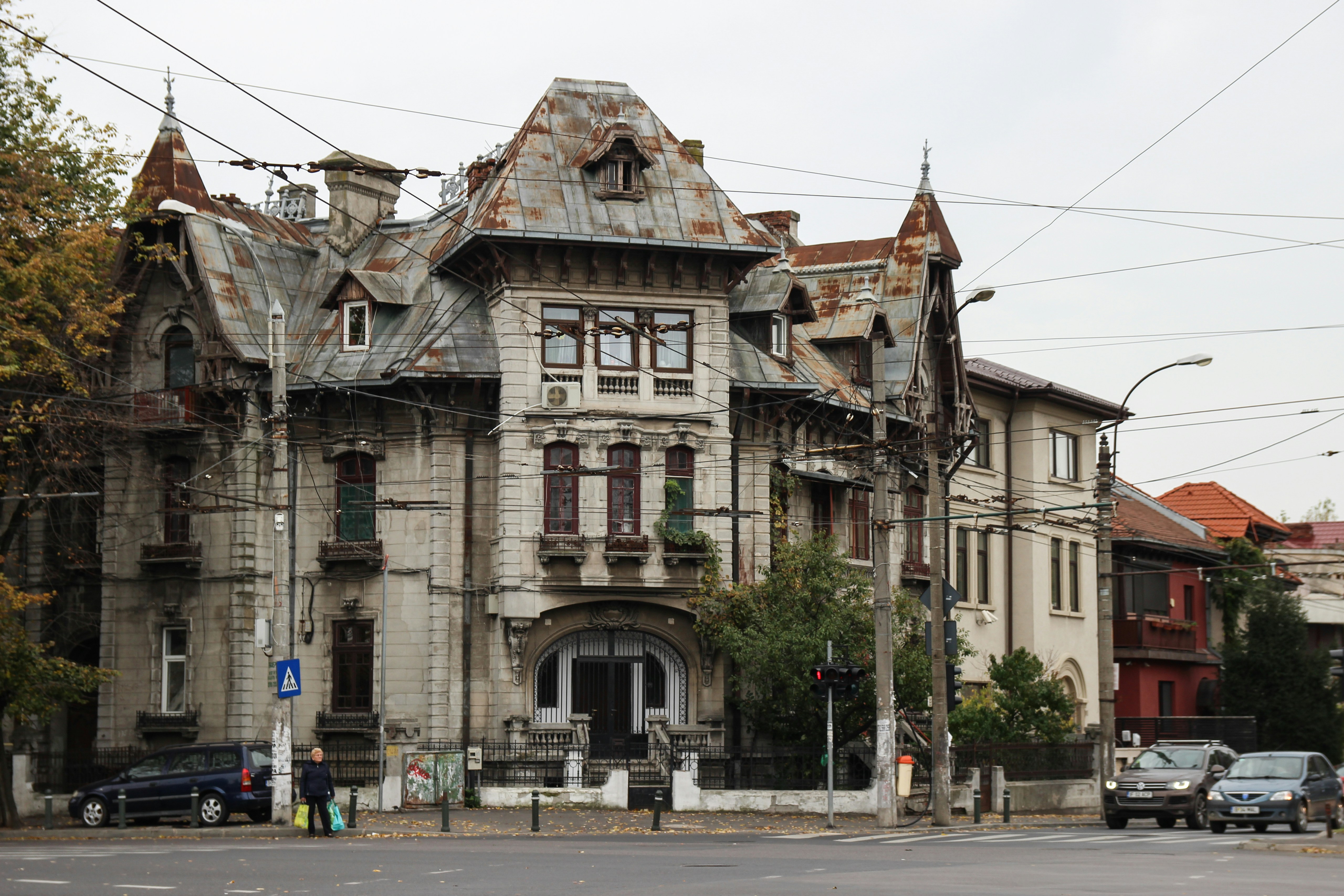 Ornate Gothic Revival house with intricate roof and arched doorway, situated at a busy street intersection.