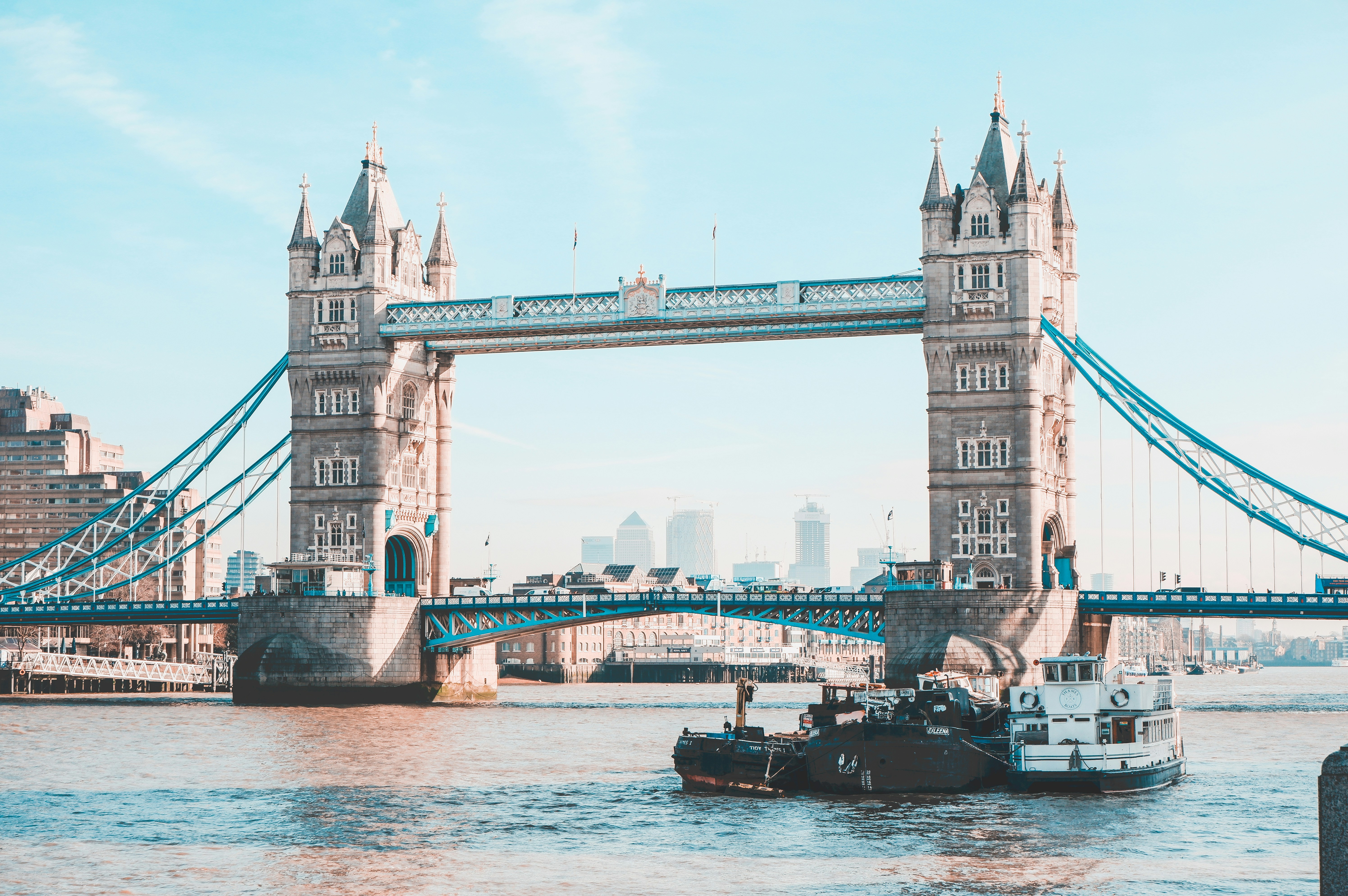 Tower Bridge stands majestically over the Thames, flanked by boats and the skyline of London. The scene captures a serene moment amidst the city's bustling life.