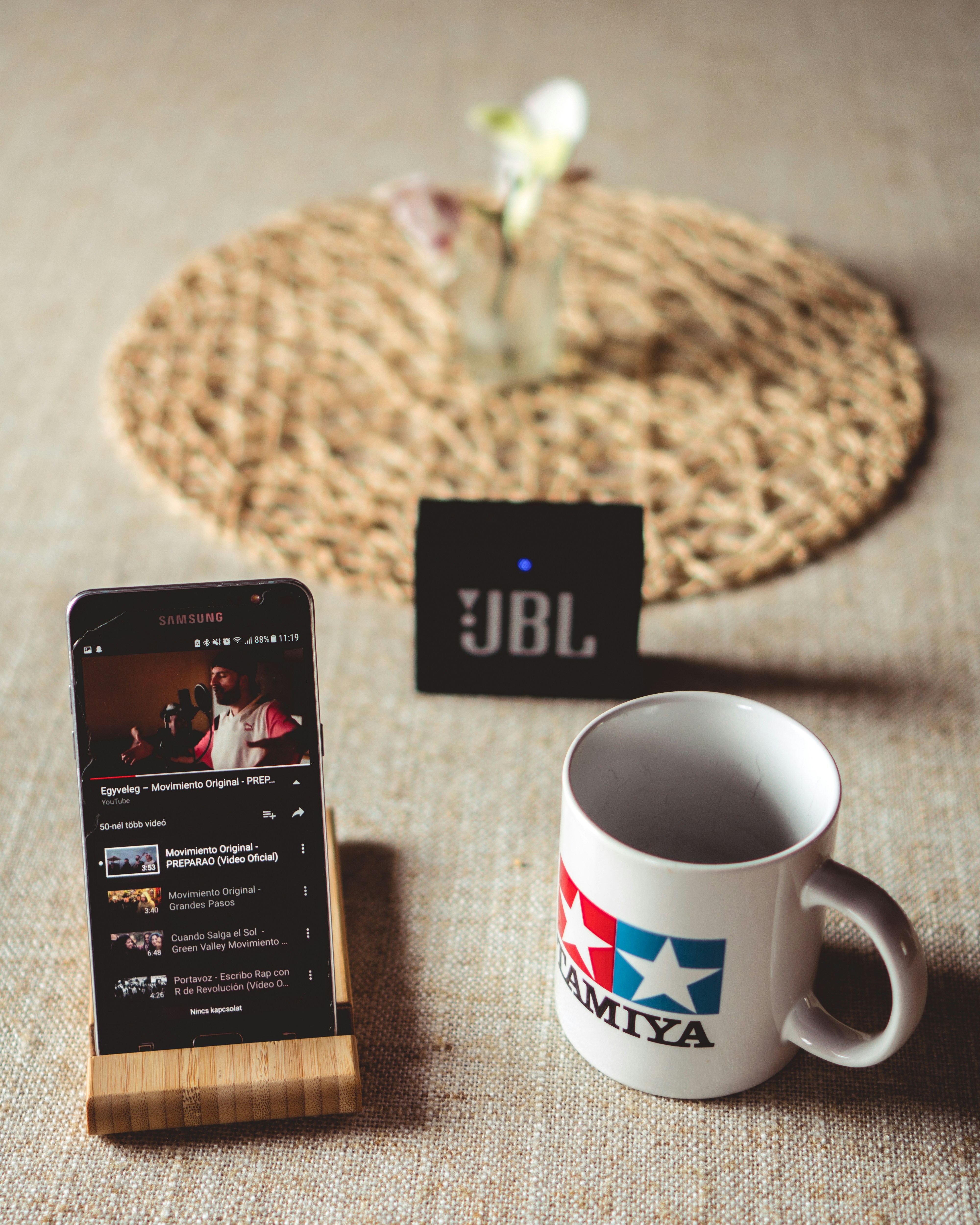 Black Samsung smartphone playing video beside white ceramic mug and ...