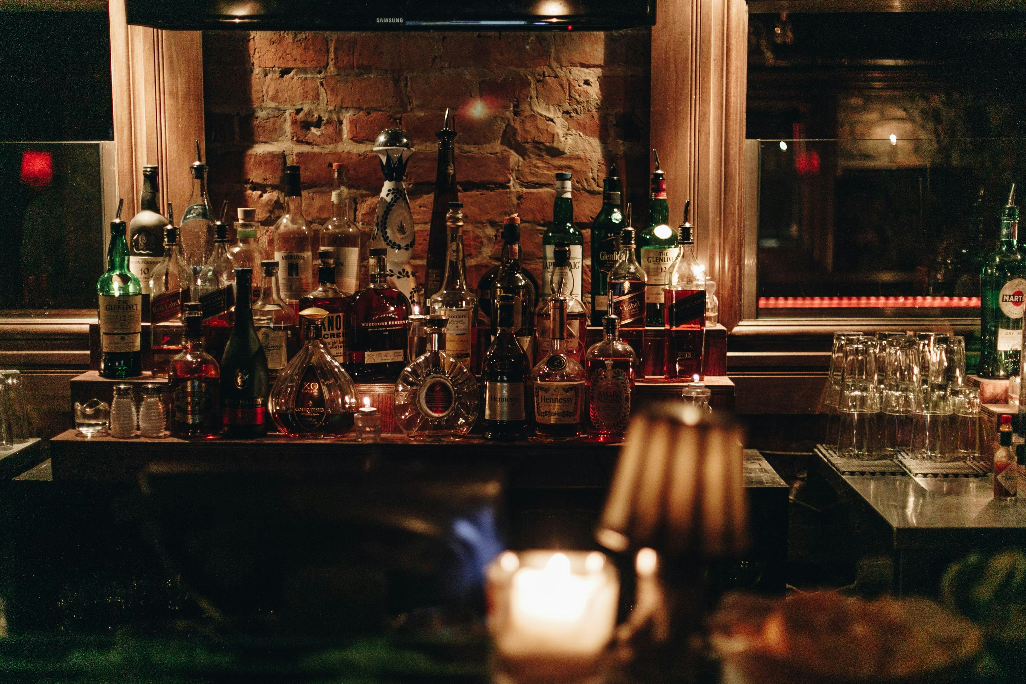 A well-stocked bar adorned with an array of liquor bottles, softly illuminated by ambient lighting, creating a warm and inviting atmosphere.