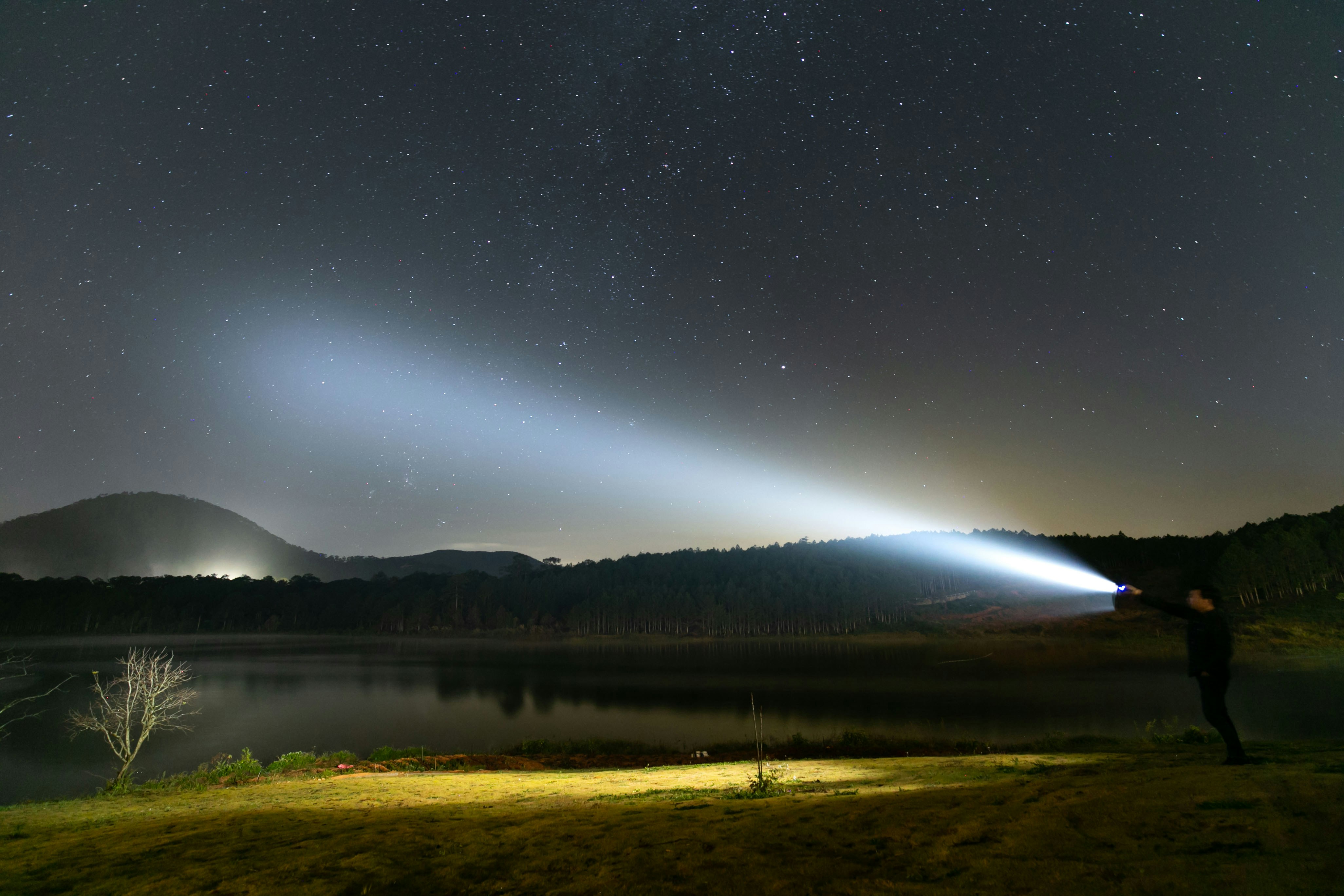 A person holding a flashlight in front of a lake photo – Free Night ...