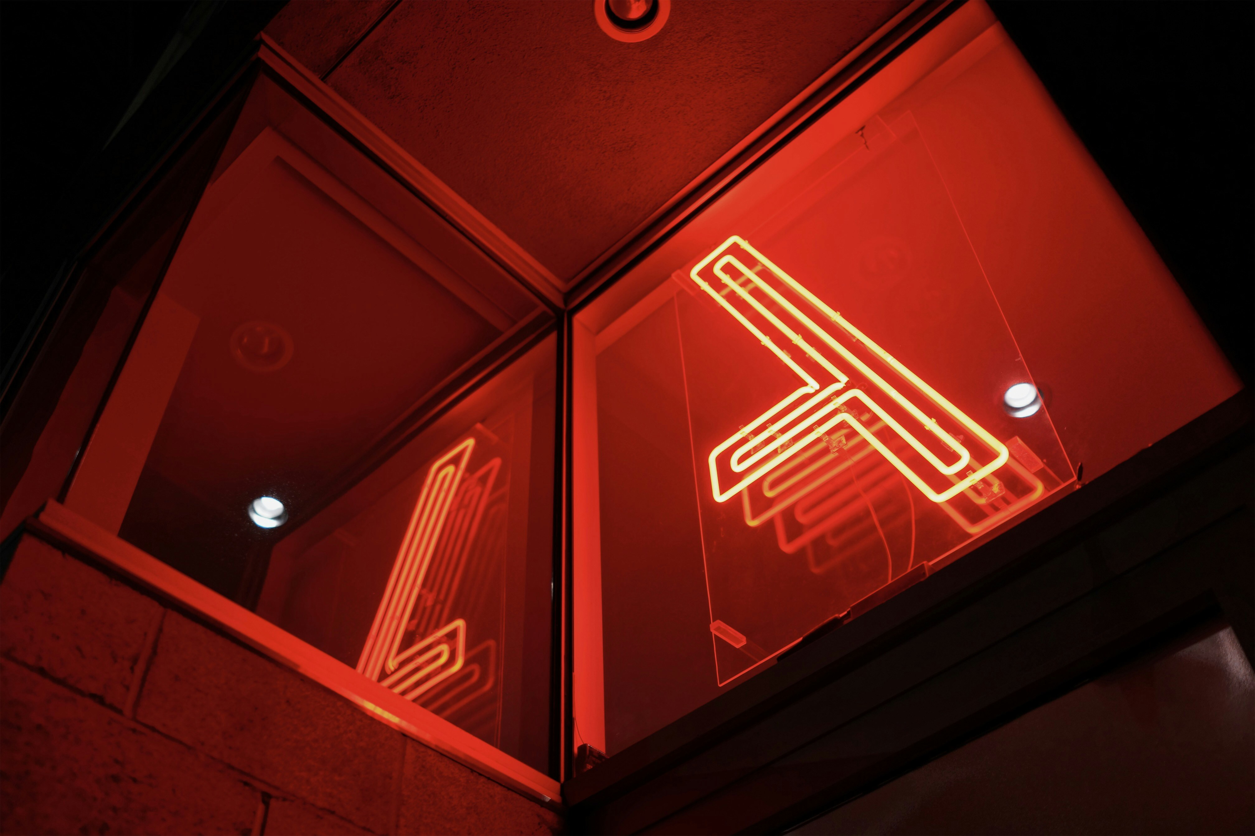 Bright red neon sign featuring angular shapes illuminating the corner of a building at night.