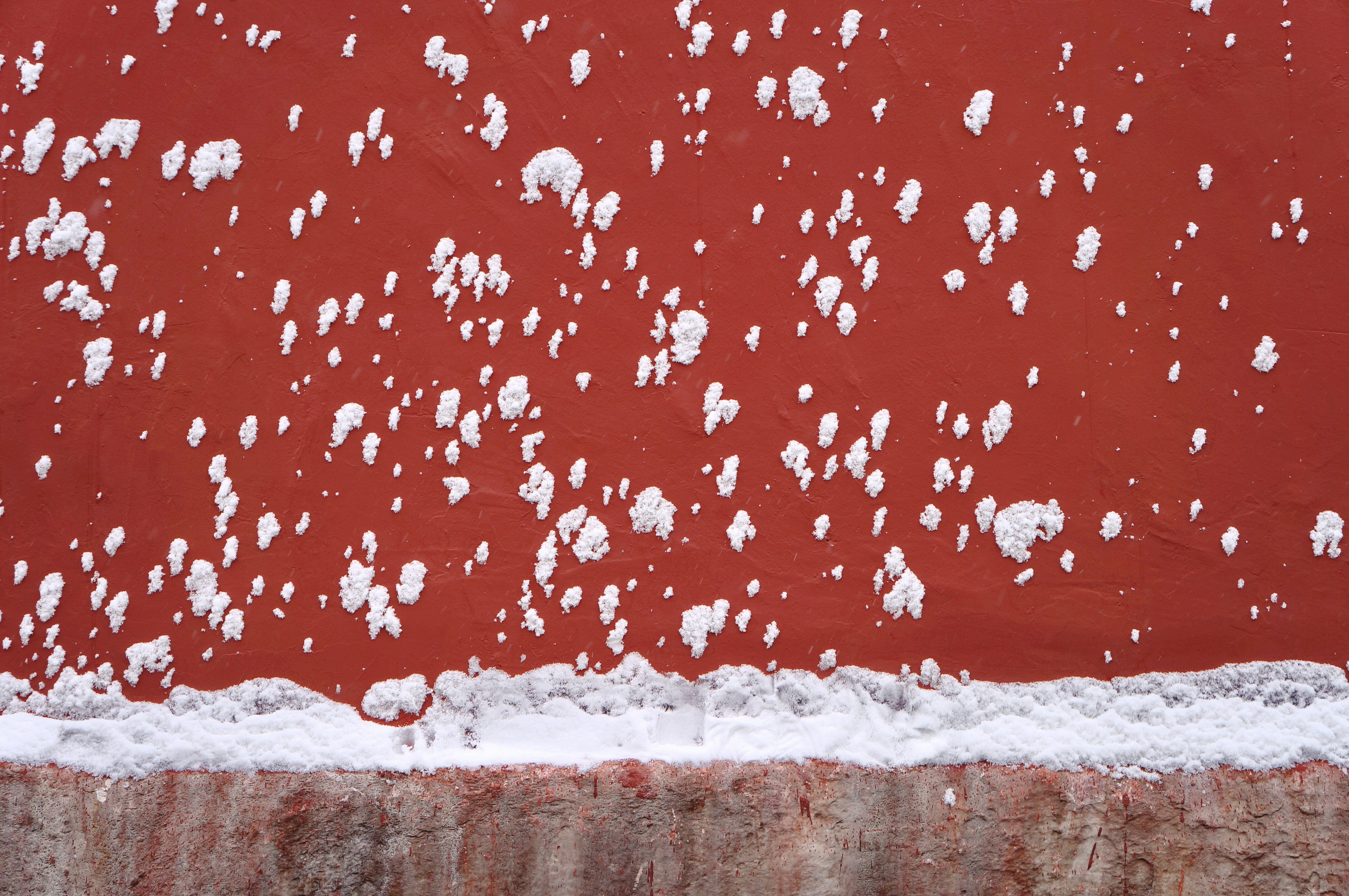 Textured red wall adorned with patches of white snow and frost, creating a striking contrast. The scene highlights the interplay between natural elements and urban surfaces.